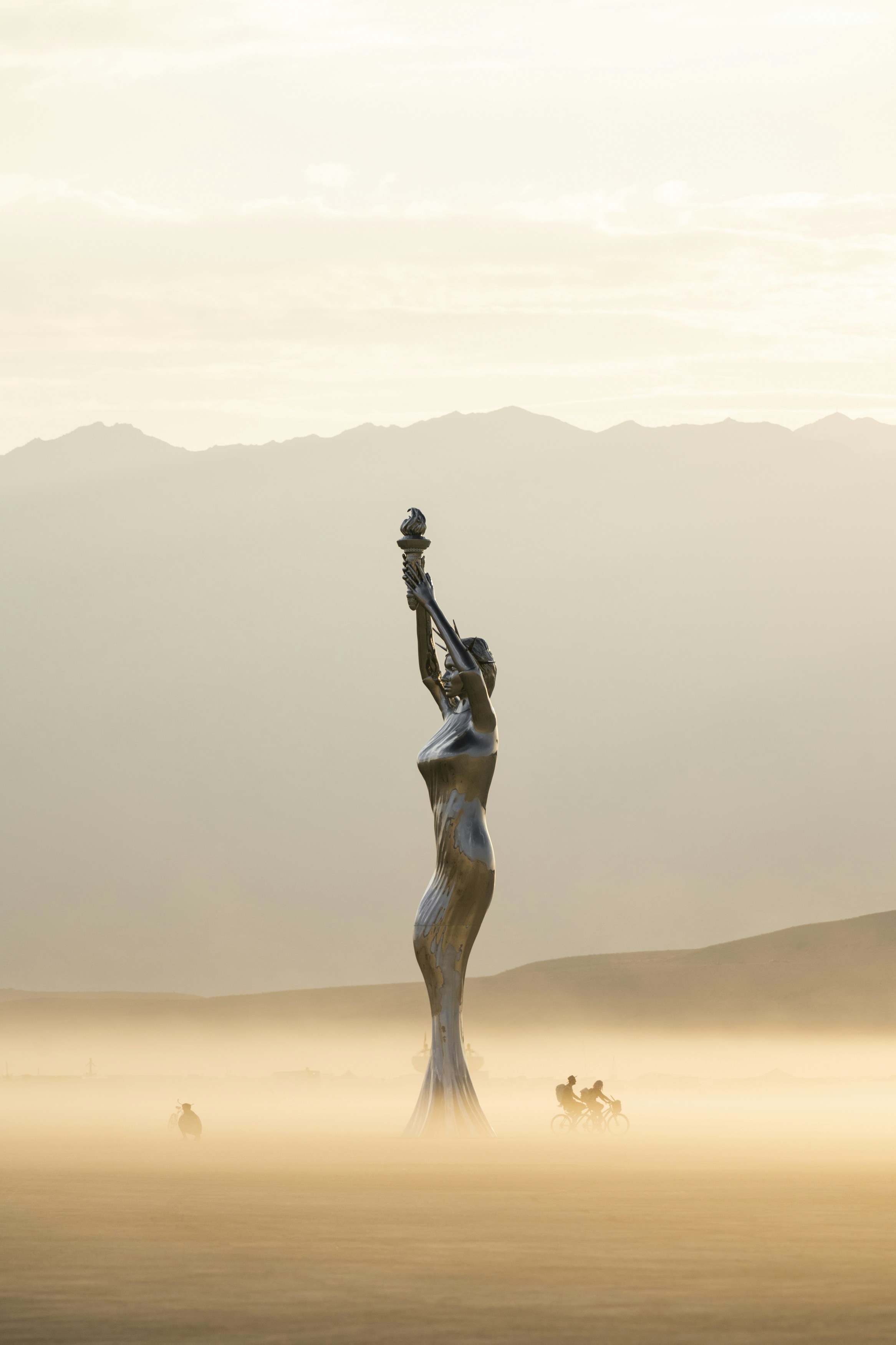 Tall sculpture emerges from a misty desert landscape with distant mountains under a soft sky.