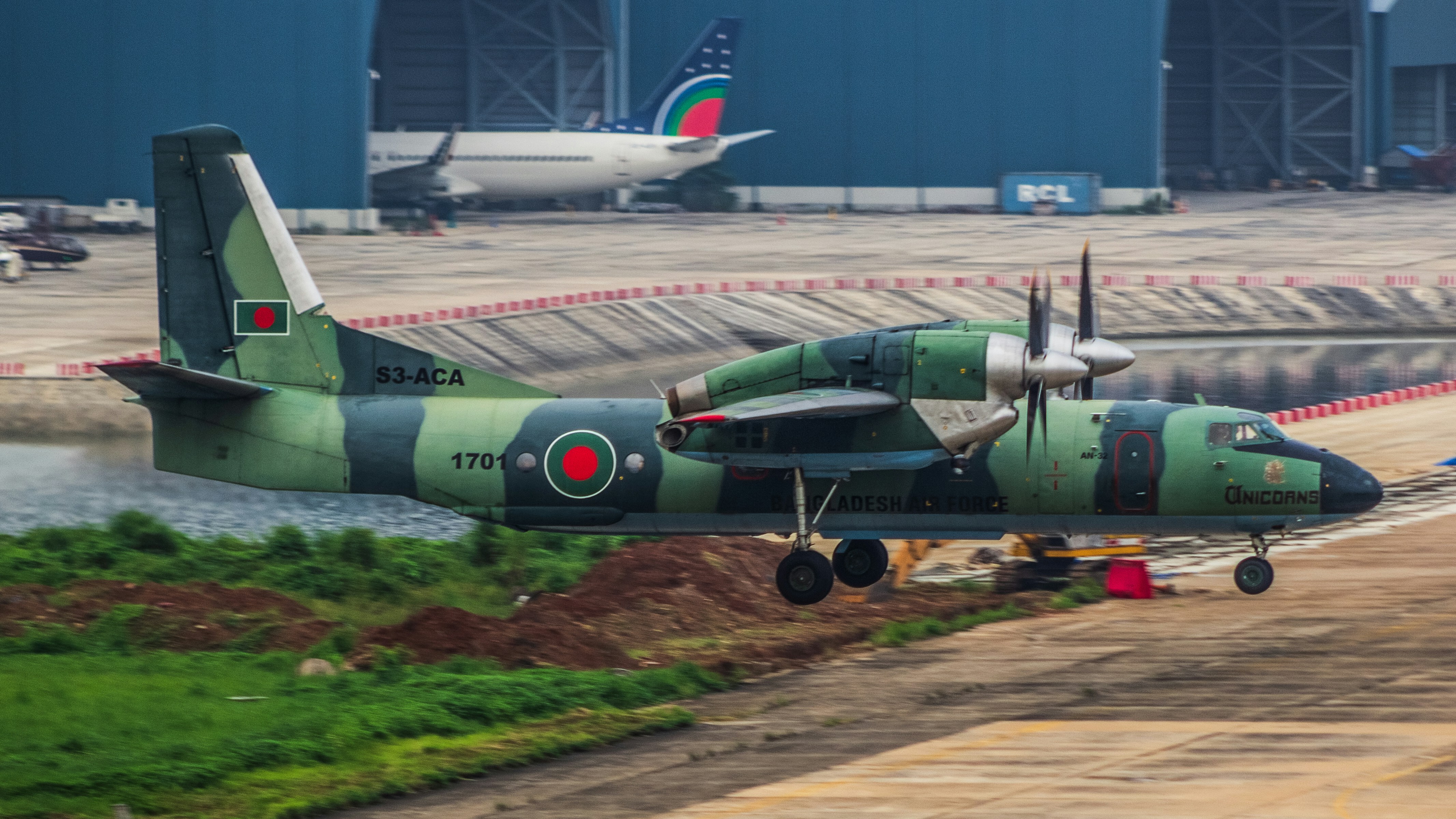 Camouflaged twin-turboprop transport on final approach along a riverfront airfield