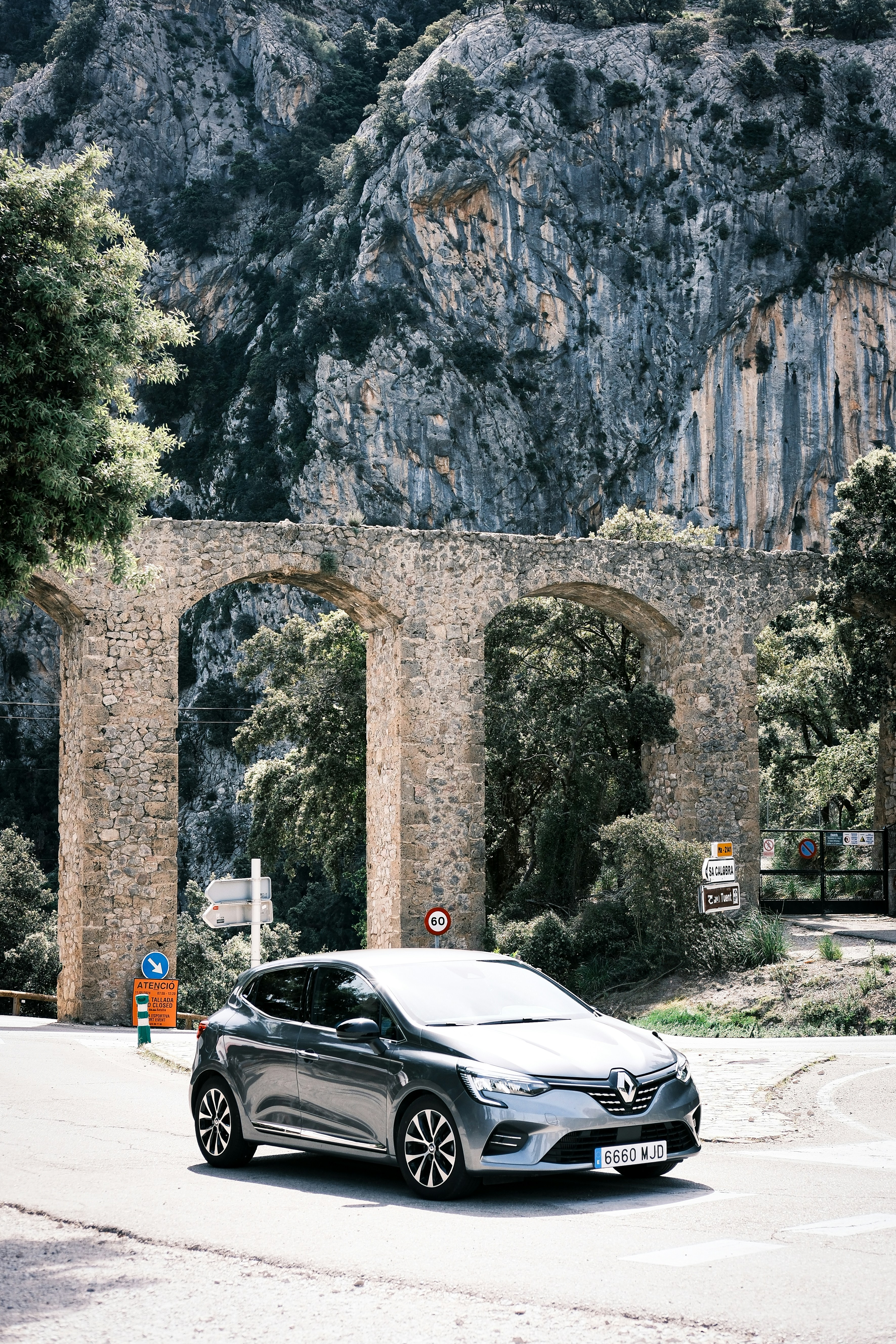 Silver Renault beneath limestone arches on a sunlit mountain road