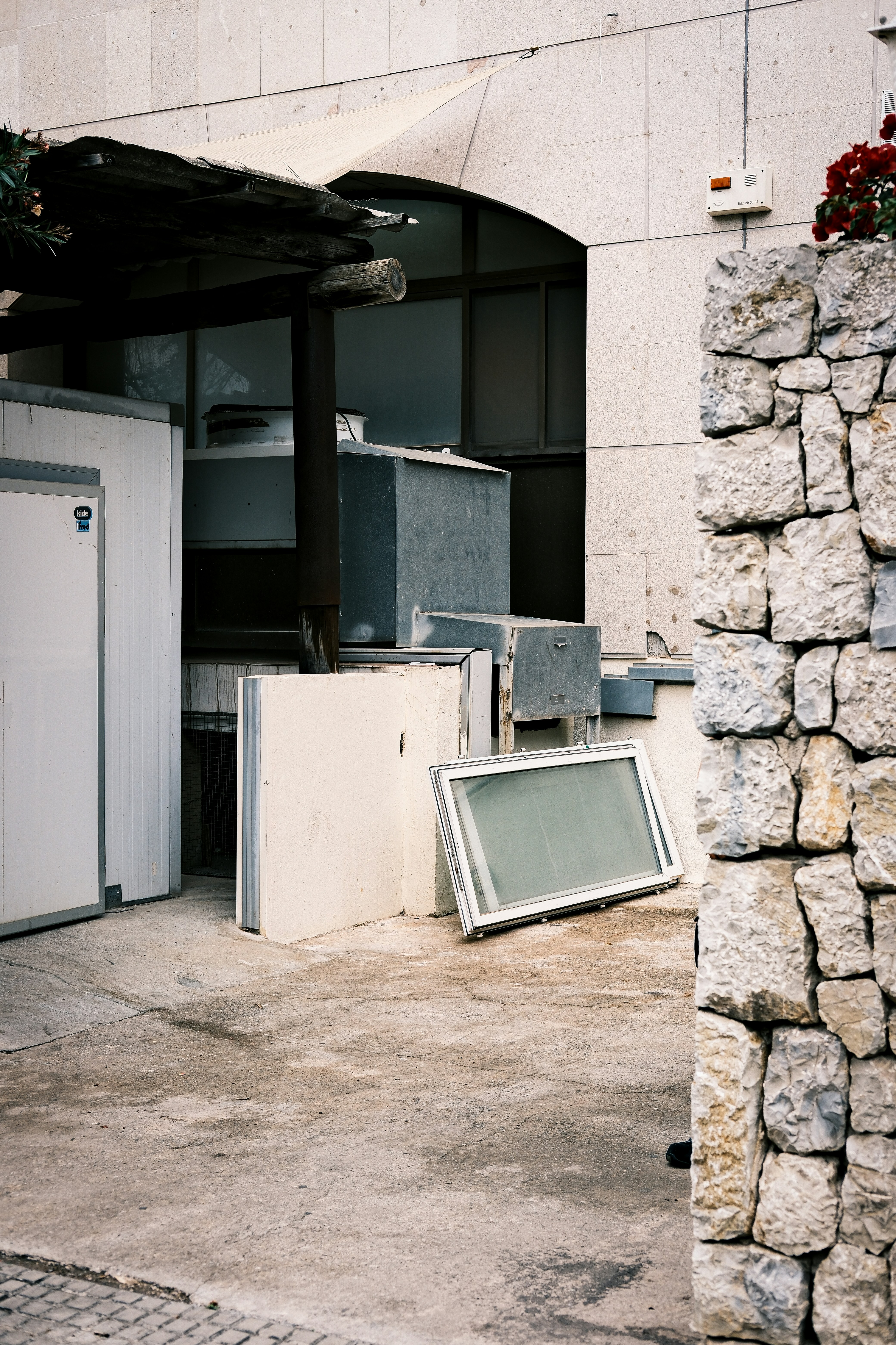Tilted Window Frame among Dismantled Utility Clutter by a Weathered Stone Wall