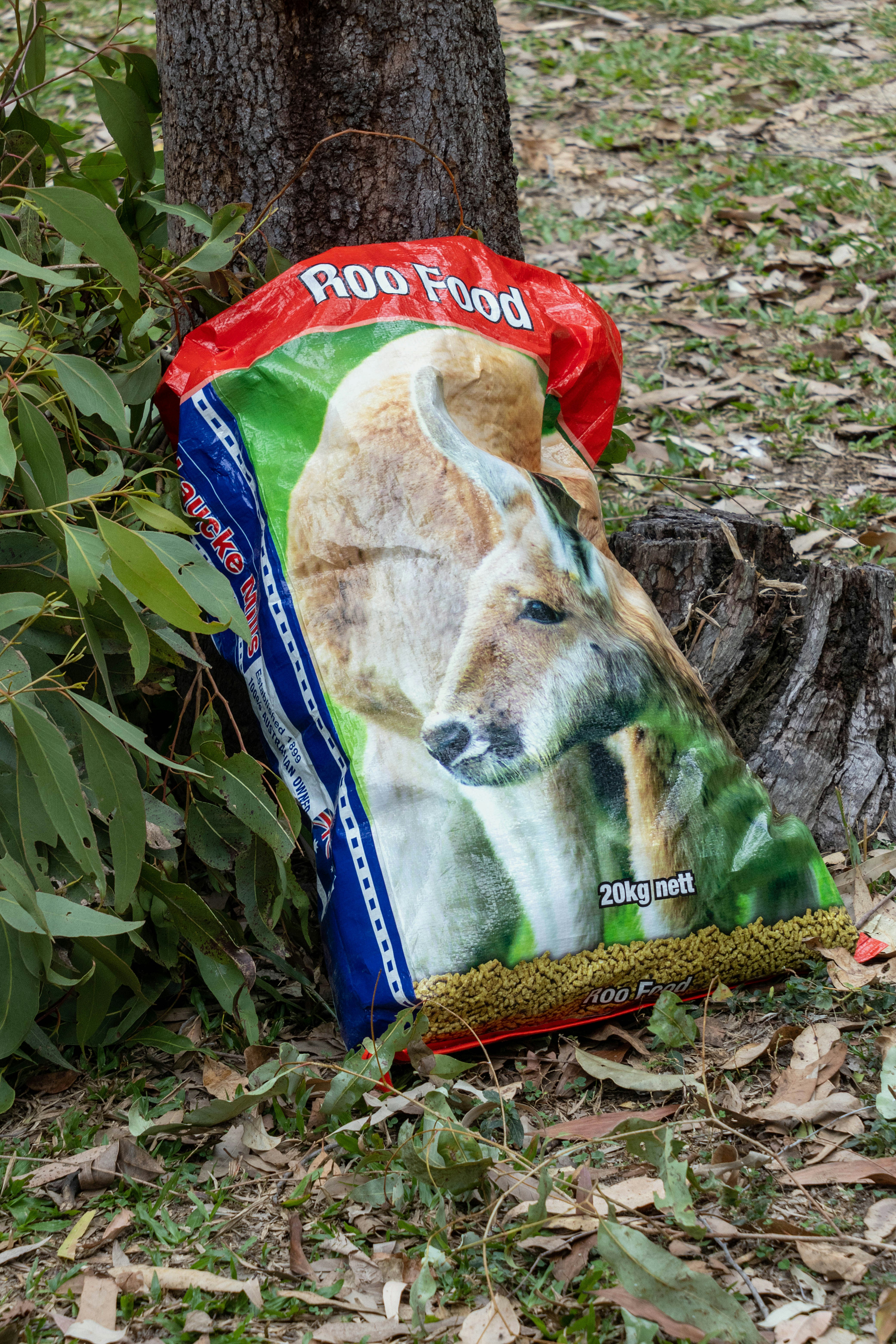 A bag of 'Roo Food' resting against a tree, showcasing a kangaroo on the packaging amidst a natural setting.