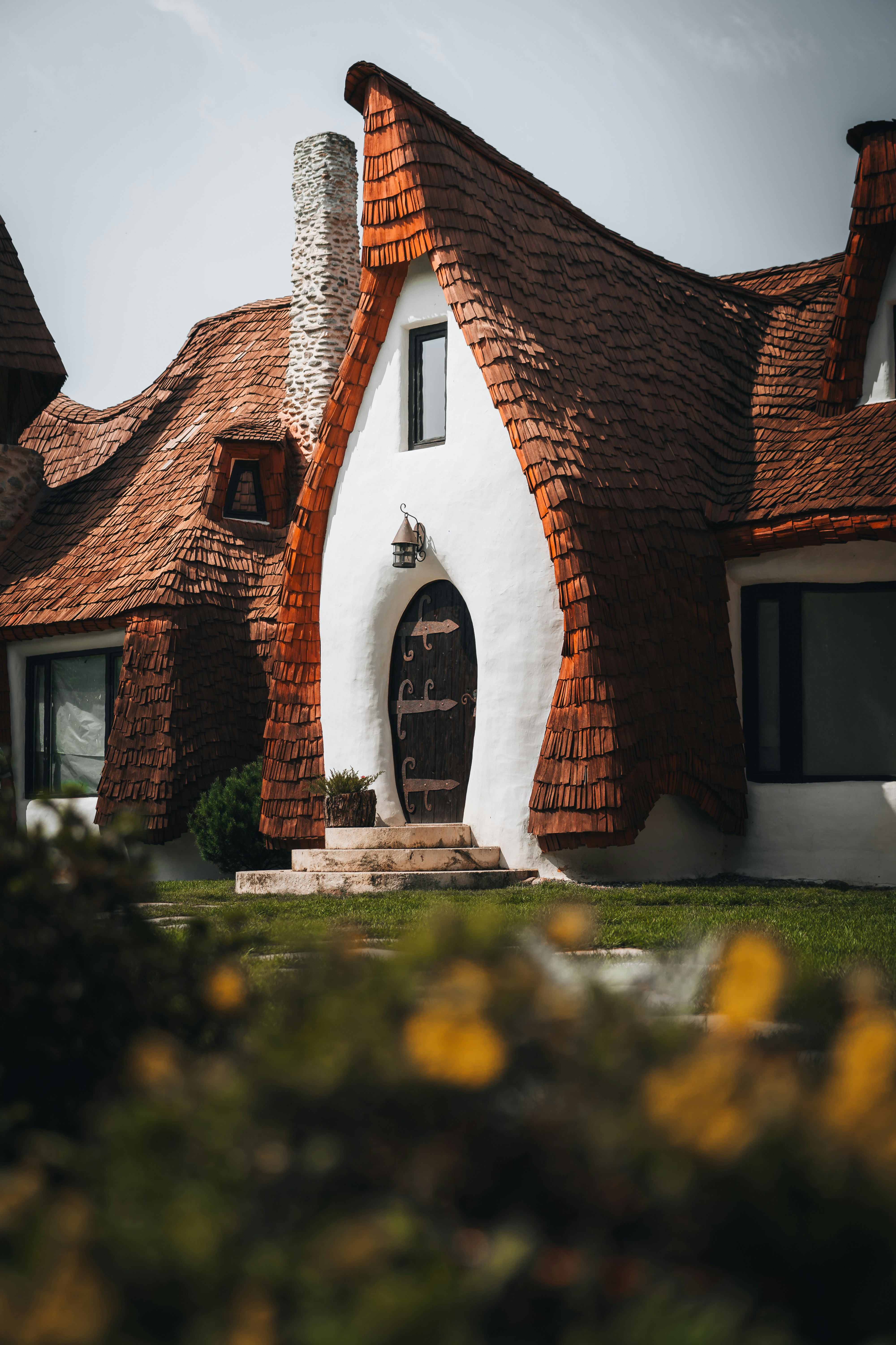 Fairytale-style cottage with curved red-tiled roofs and a central rounded entrance under a cloudy sky.