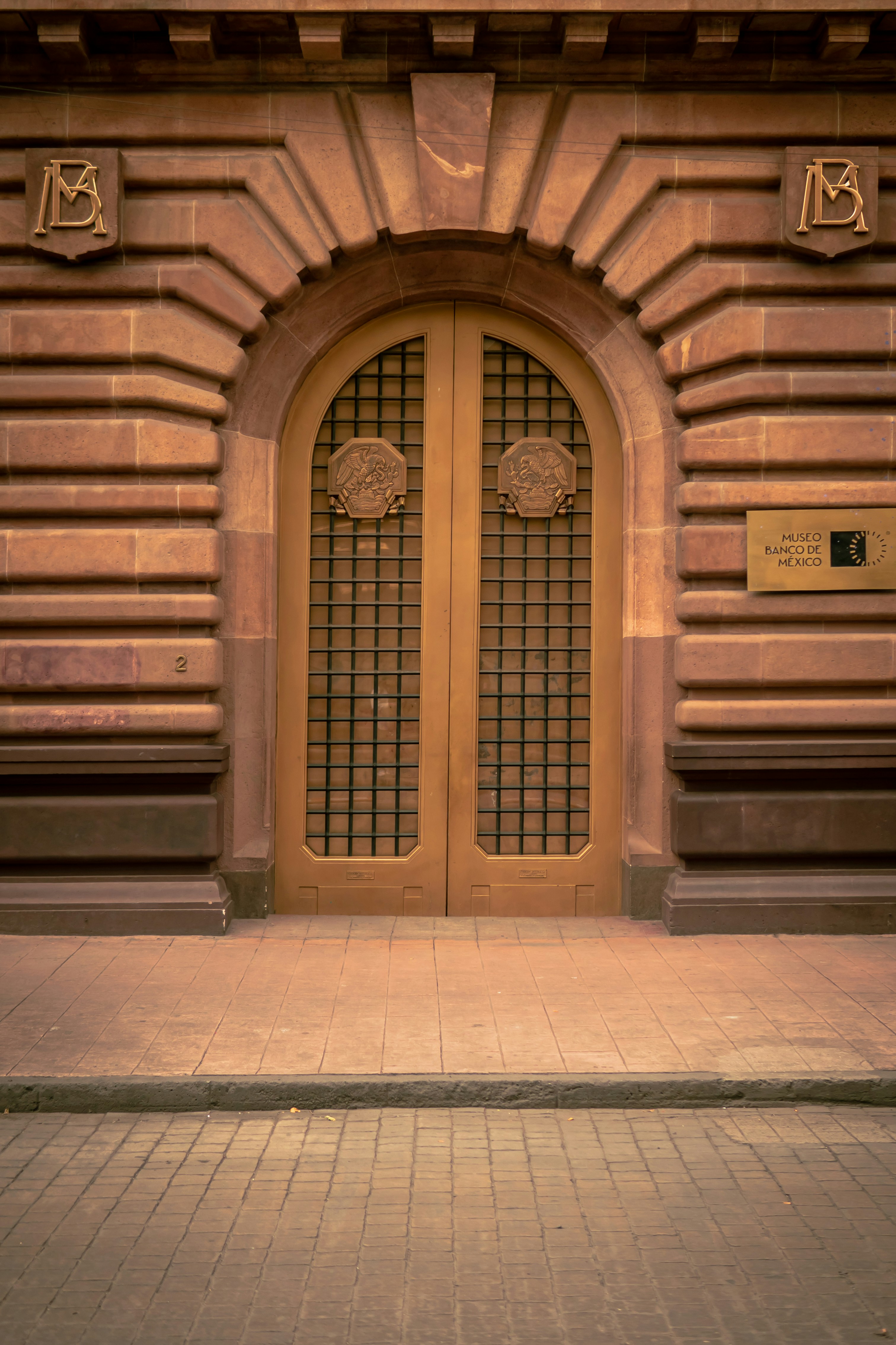 Intricately designed entrance doors of a historic building, showcasing ornate carvings and a textured facade. A plaque identifies the Museo Banco de México.
