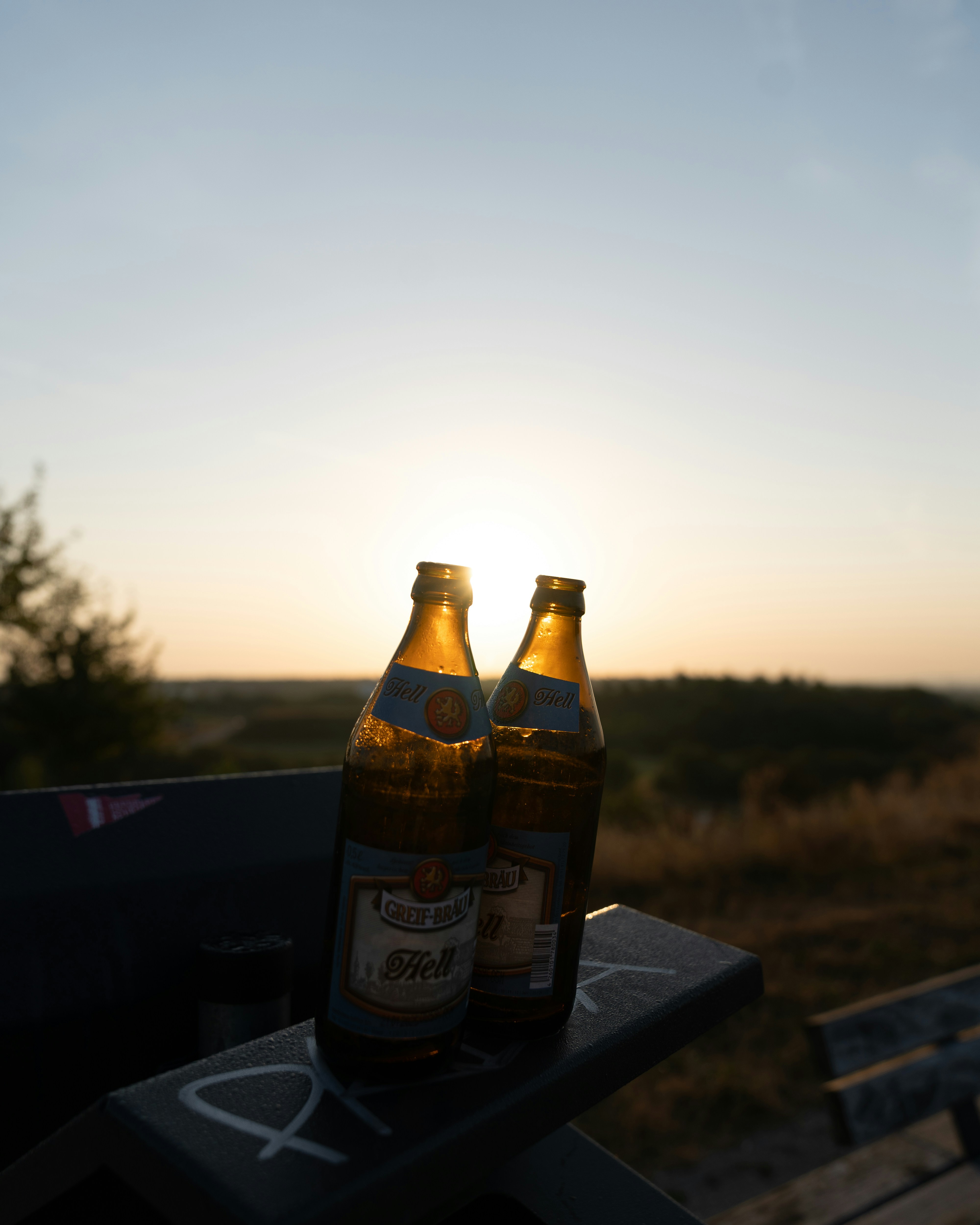 Golden Hour Bottles on a Camp Grill: Two Amber Beers at Dusk
