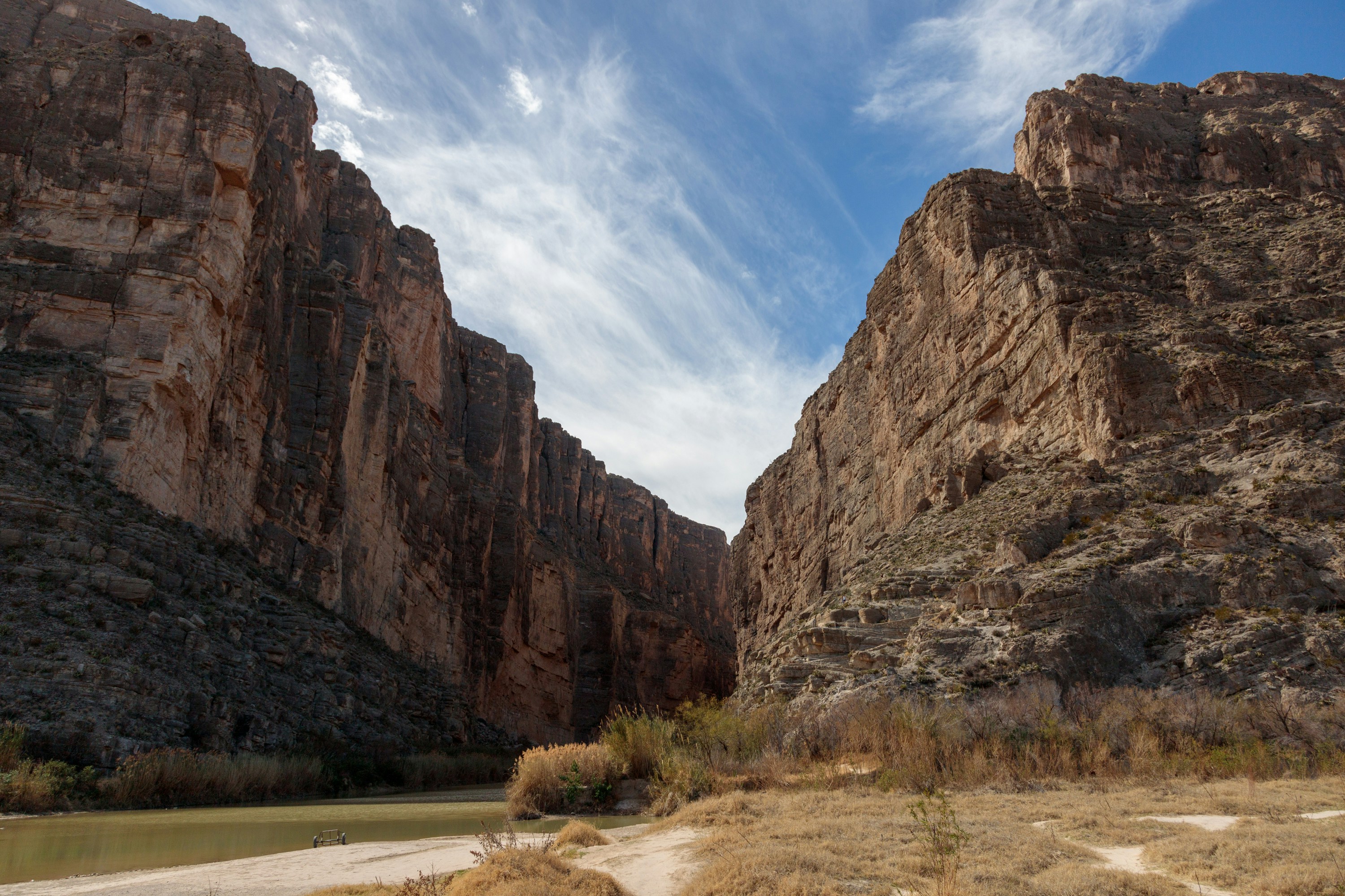 Towering rock formations frame a narrow canyon under a sky streaked with clouds.