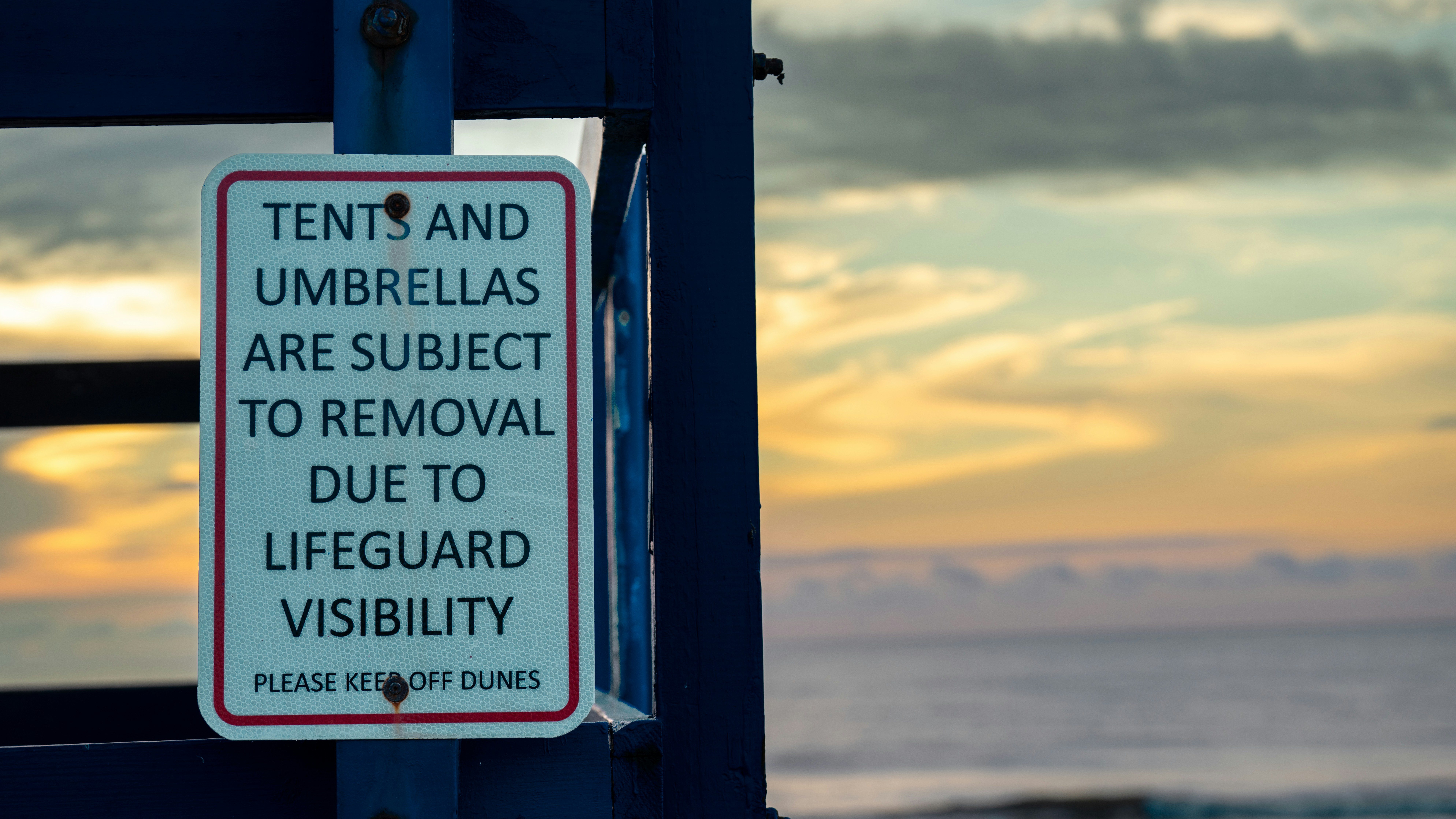 Sunset Signpost: Lifeguard Visibility Warning on a Blue Pier