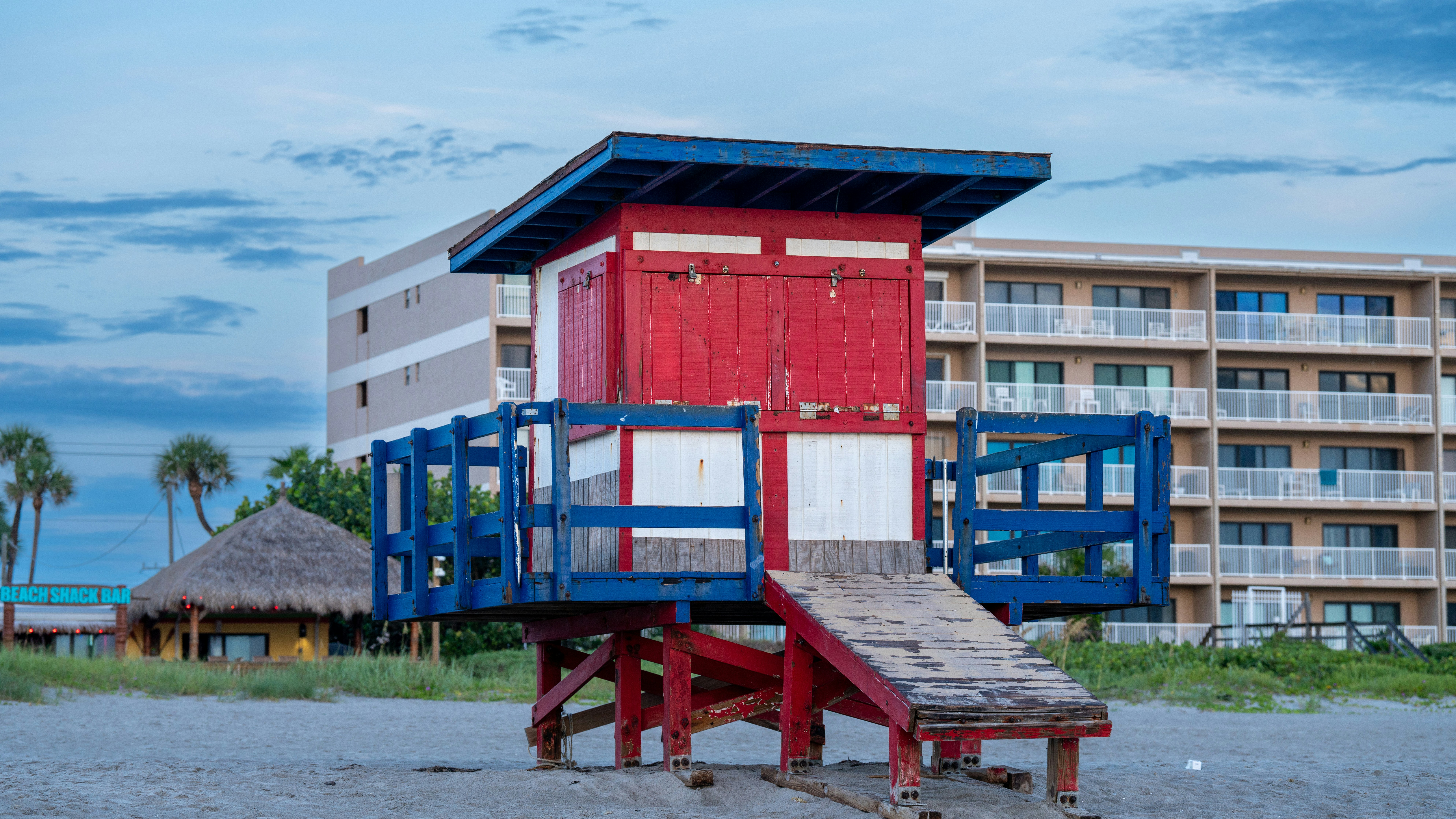 A red and blue lifeguard tower next to a building photo – Free Beach ...