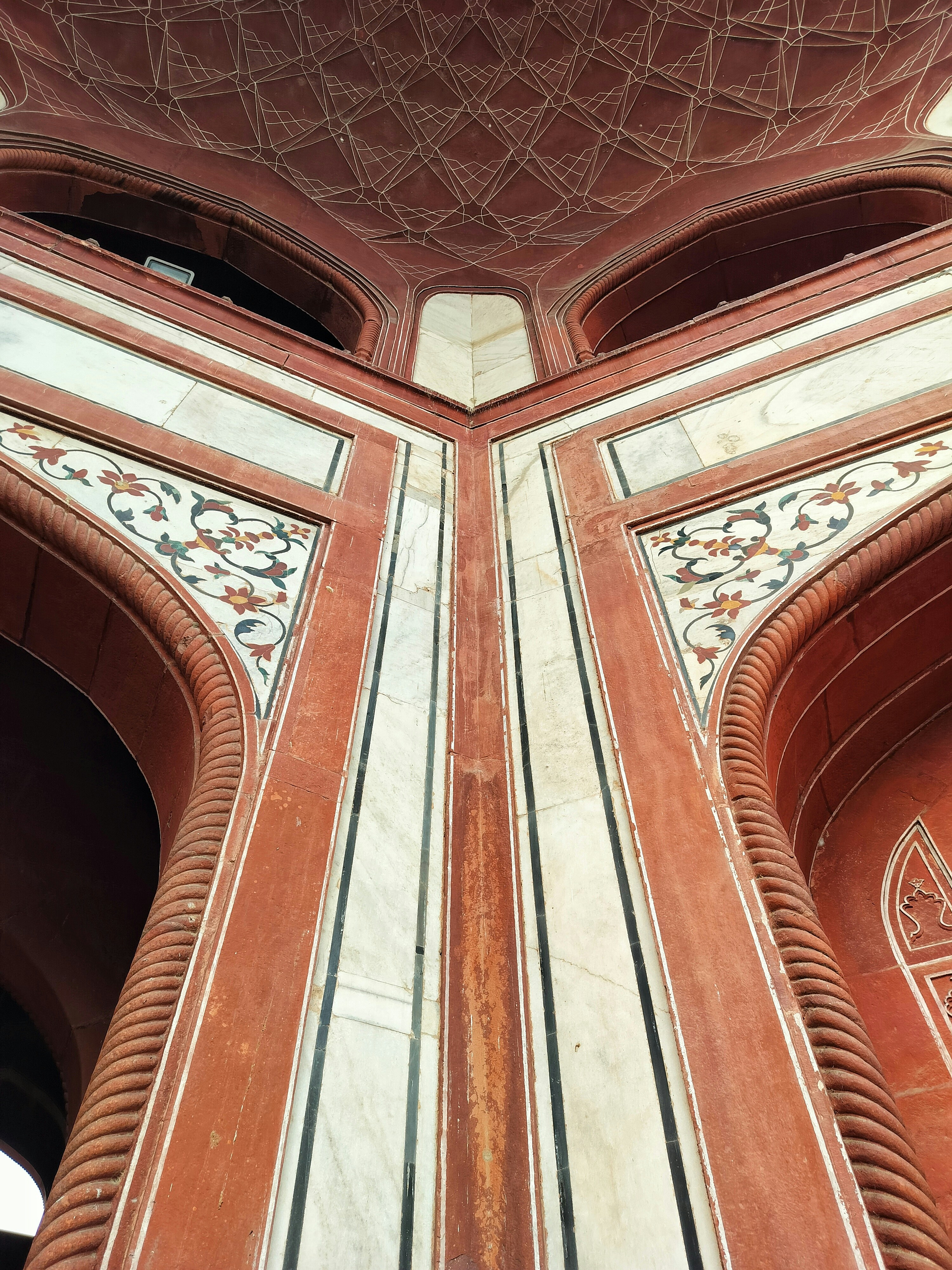 Symmetrical red sandstone arches frame white marble panels with decorative tilework, viewed from a low angle.
