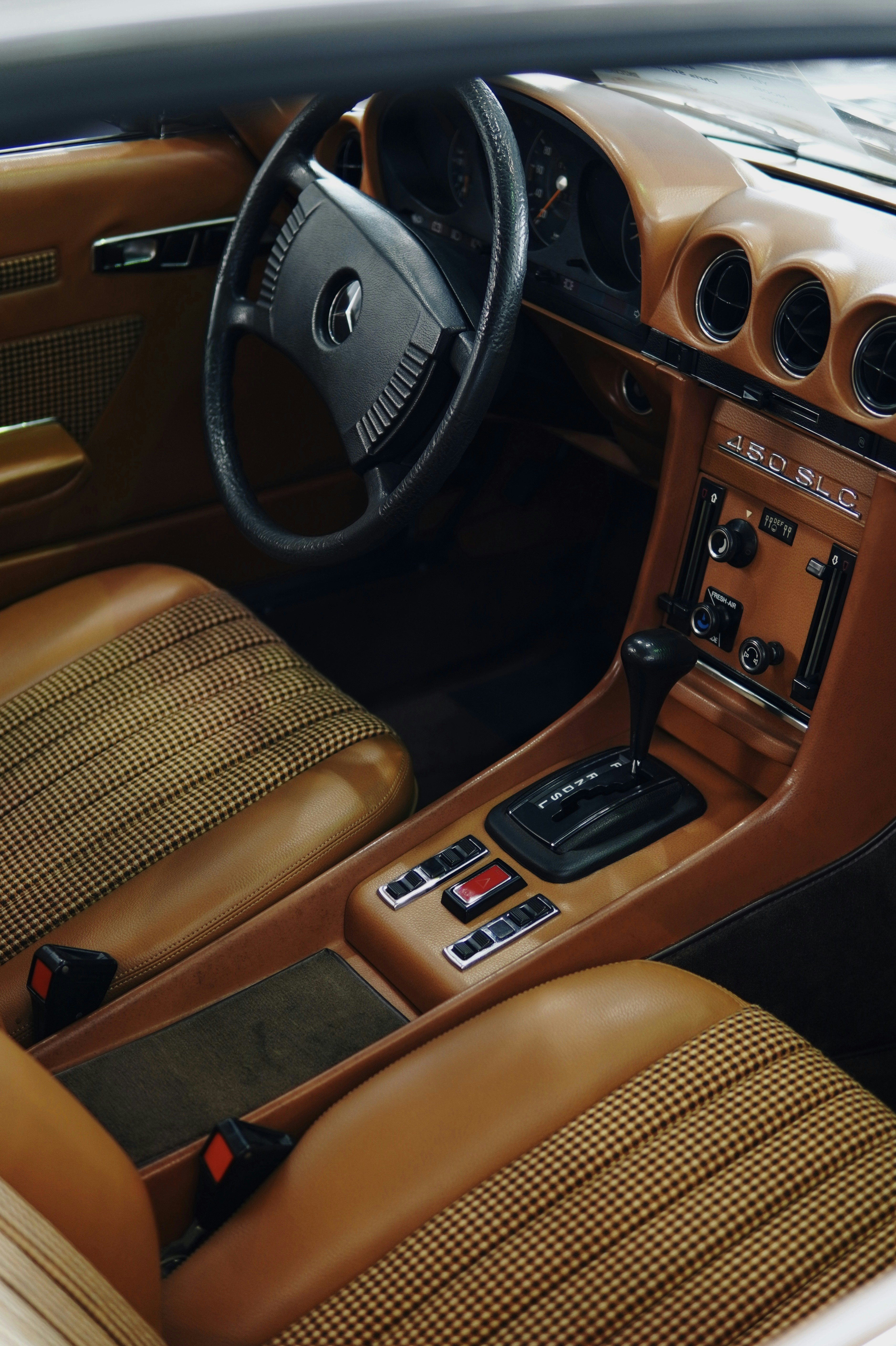 Photograph of a vintage Mercedes interior with tan leather seats, plaid upholstery, and a retro center console with an automatic gear shifter.