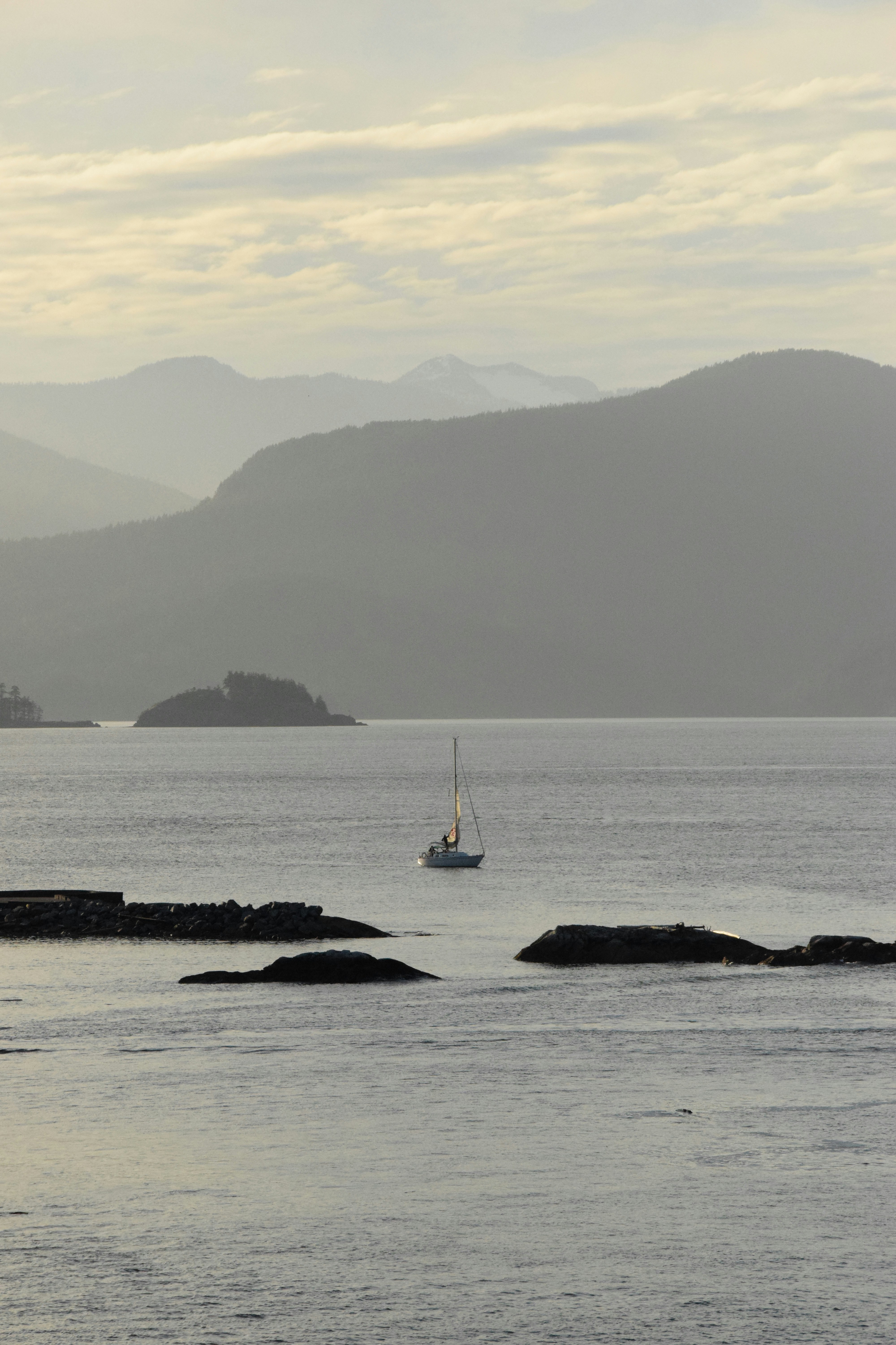 Mist-Laden Fjord: A Sailboat Lingers on Quiet Waters