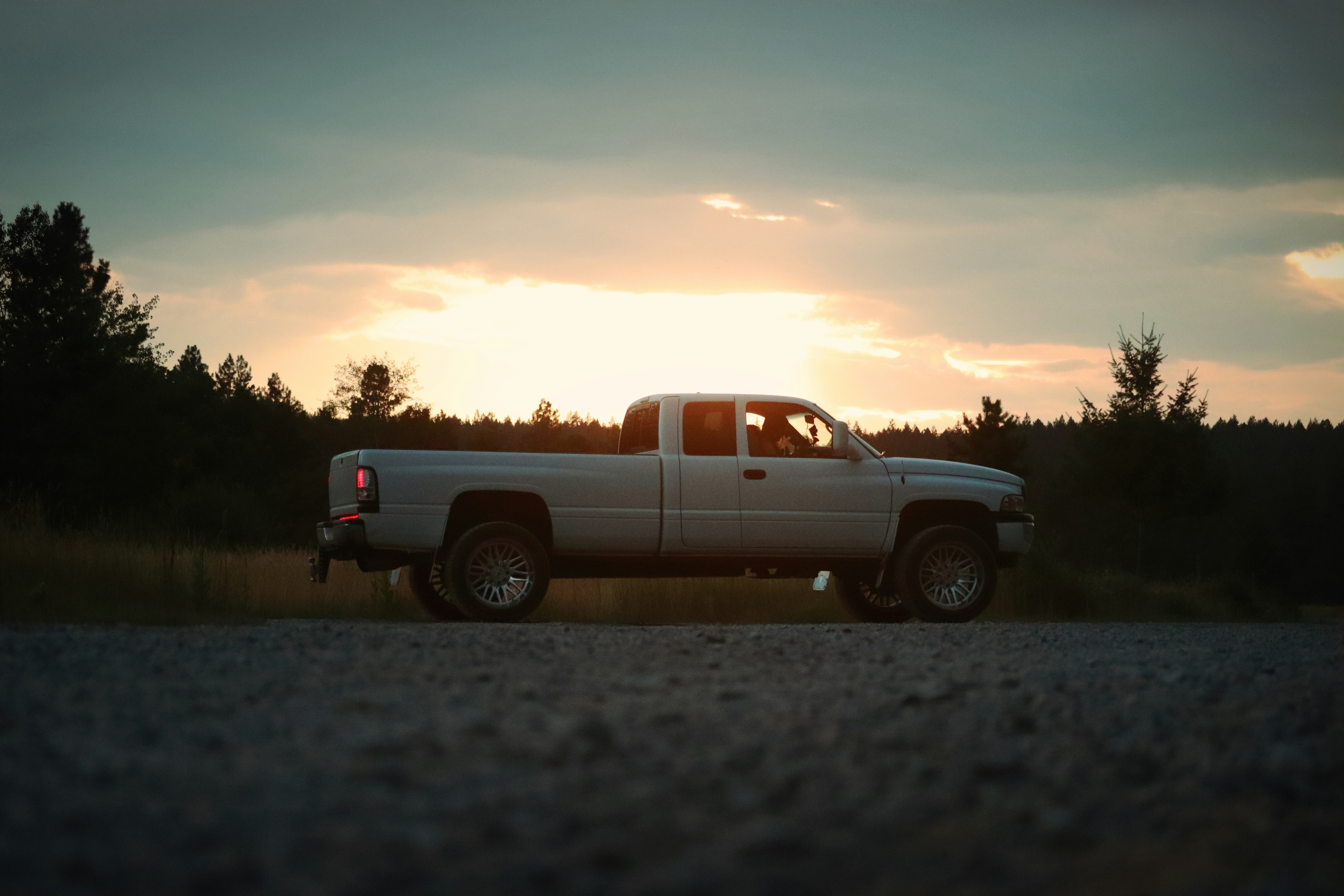 Gravel Road Dusk: White Pickup Silhouette Against a Golden Horizon