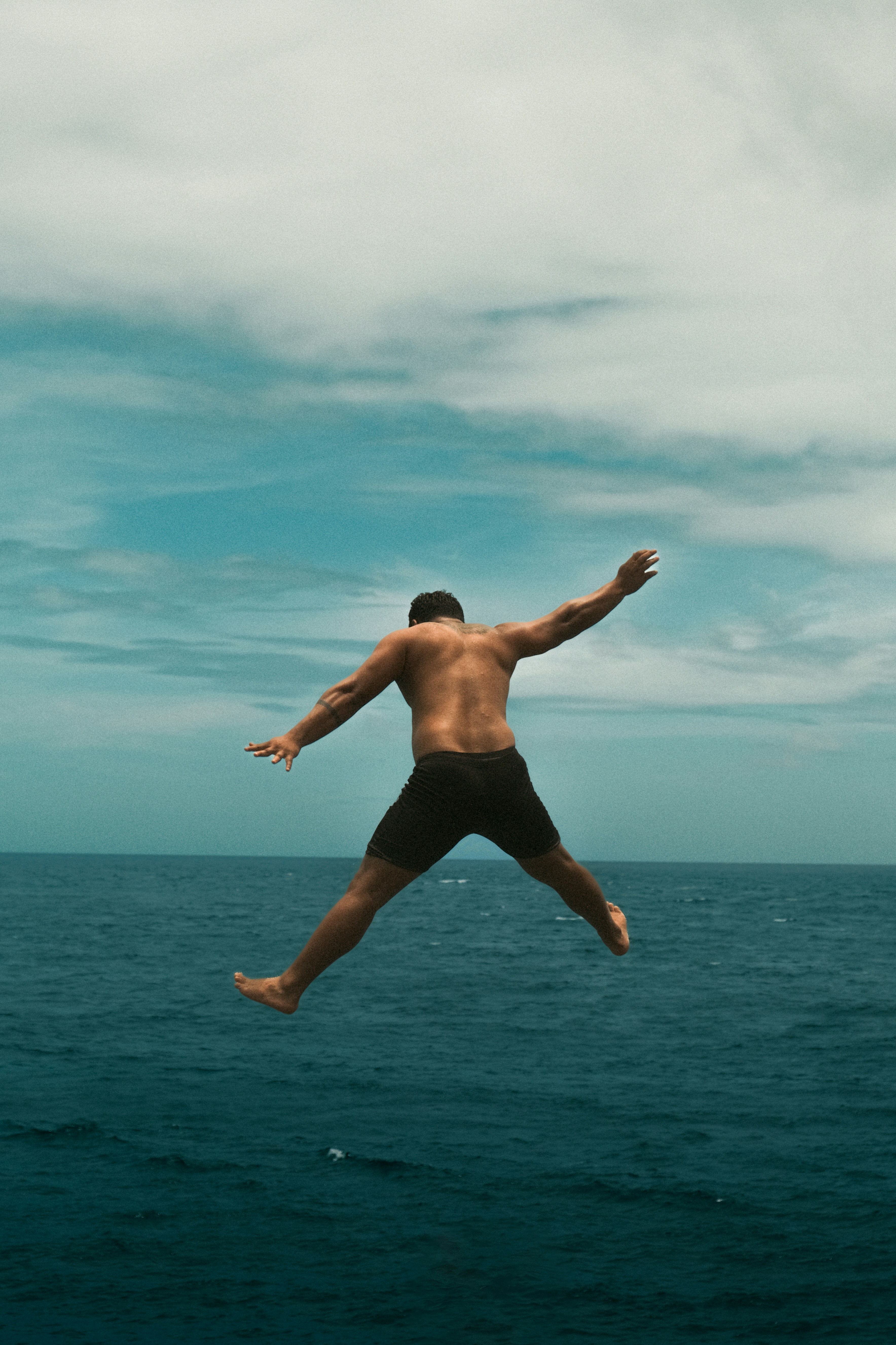 Azure Leap: A Shirtless Jumper Soars Over the Open Sea