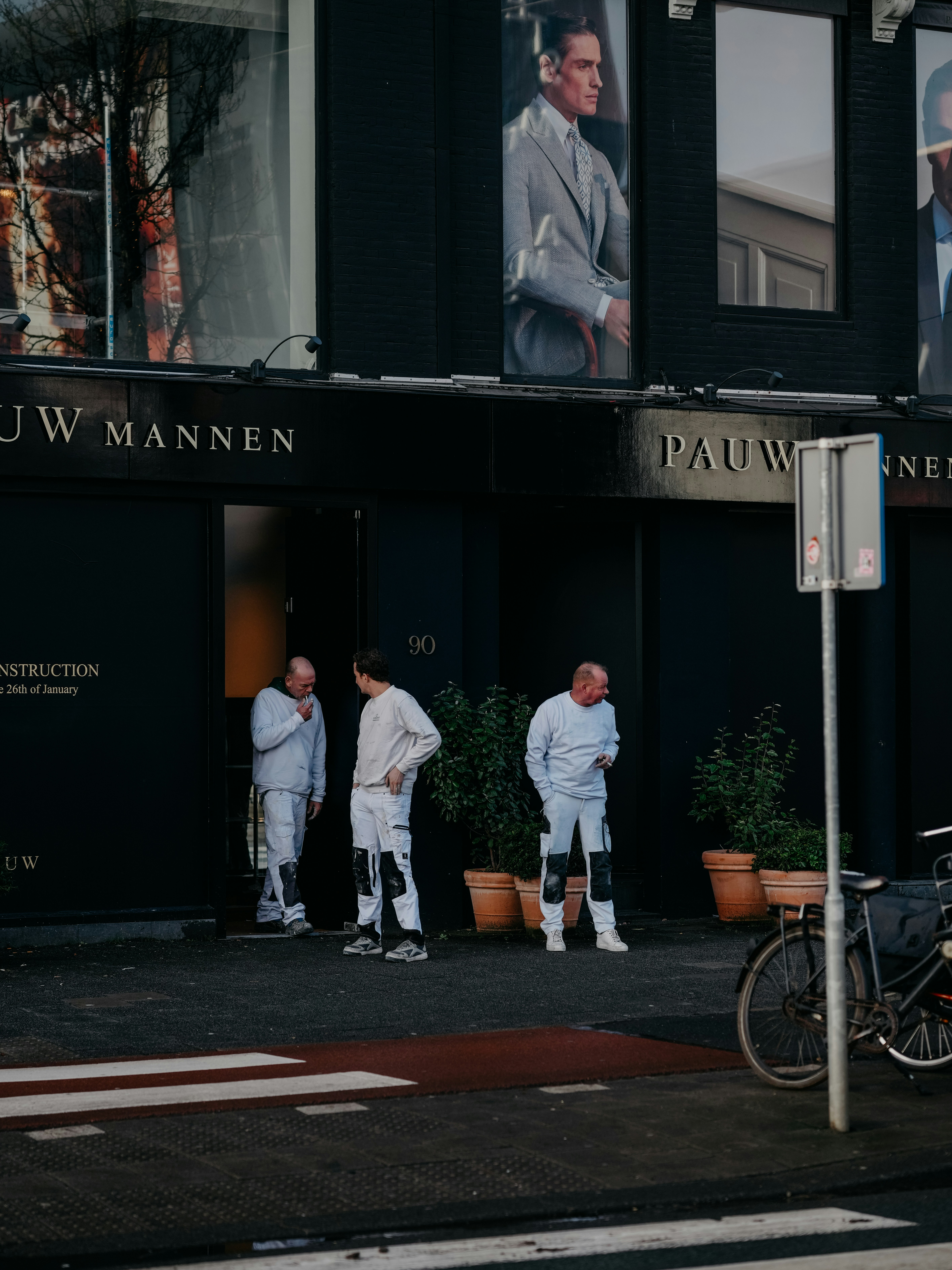 Three pale-blue life-size cutouts anchor a quiet storefront beneath towering fashion posters