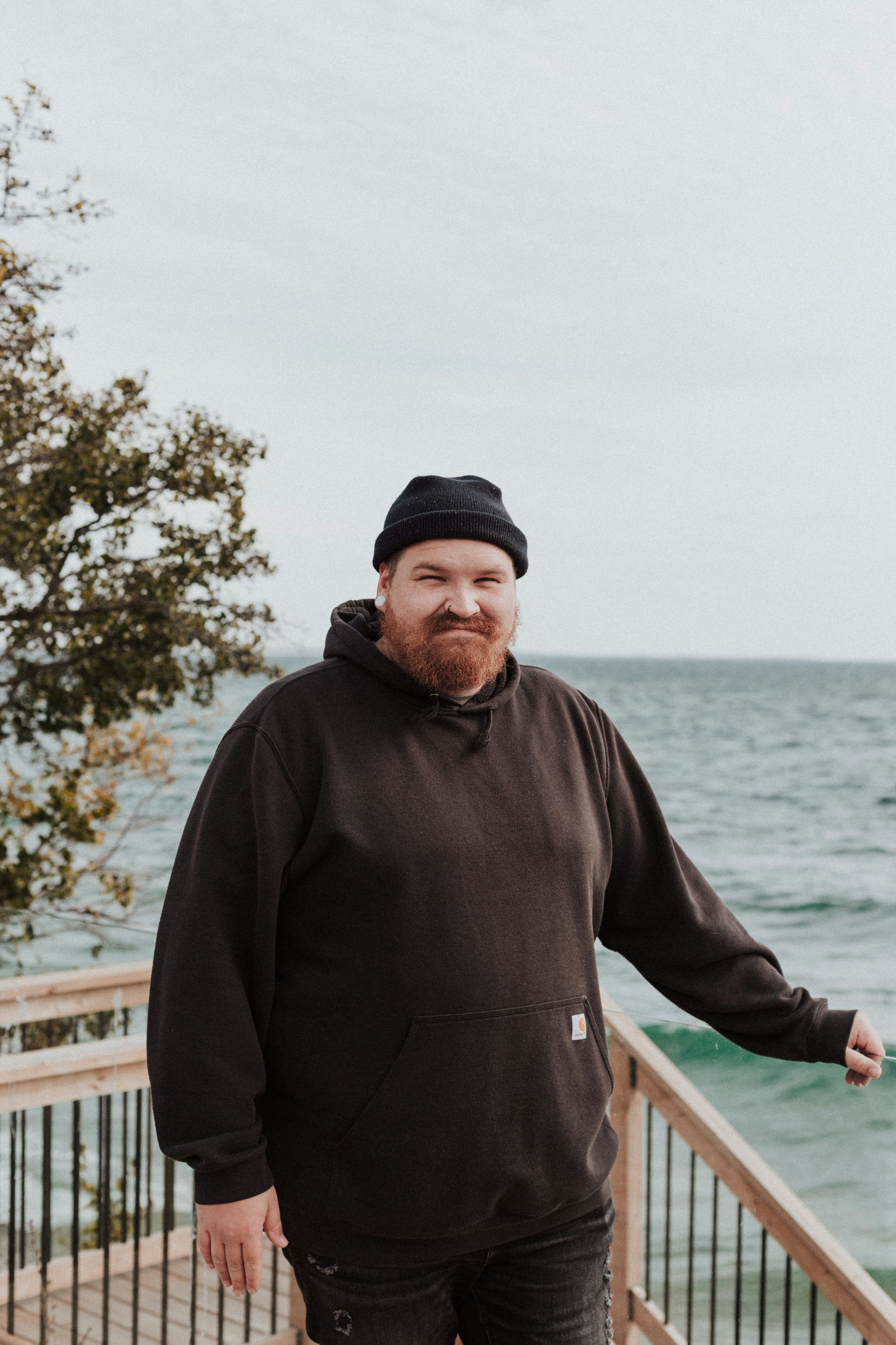 Um homem com capuz preto em pé em um deck de madeira ao lado do oceano ...