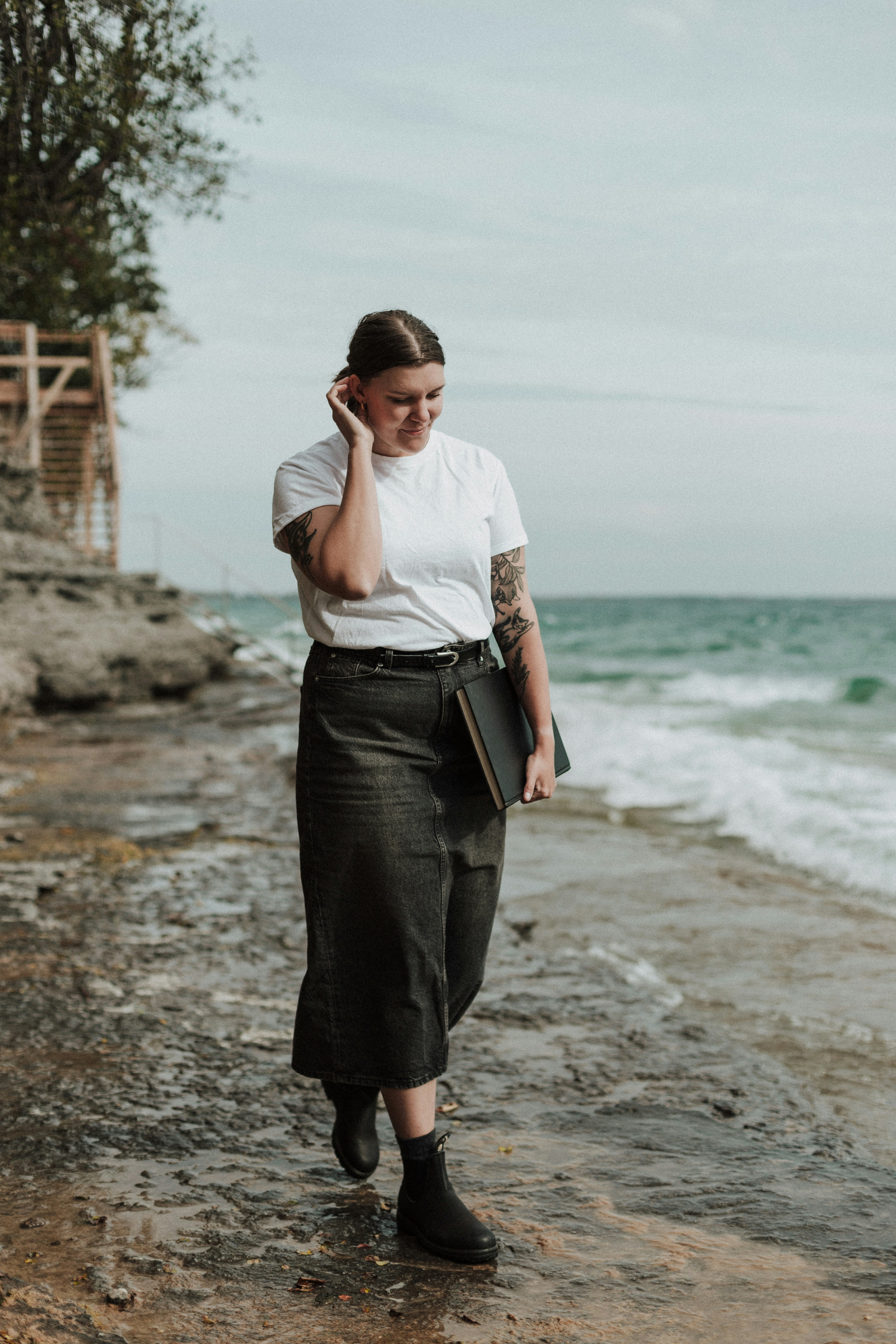 Coastal Portrait by the Break: A Woman with a Notebook Steps Along the Shore