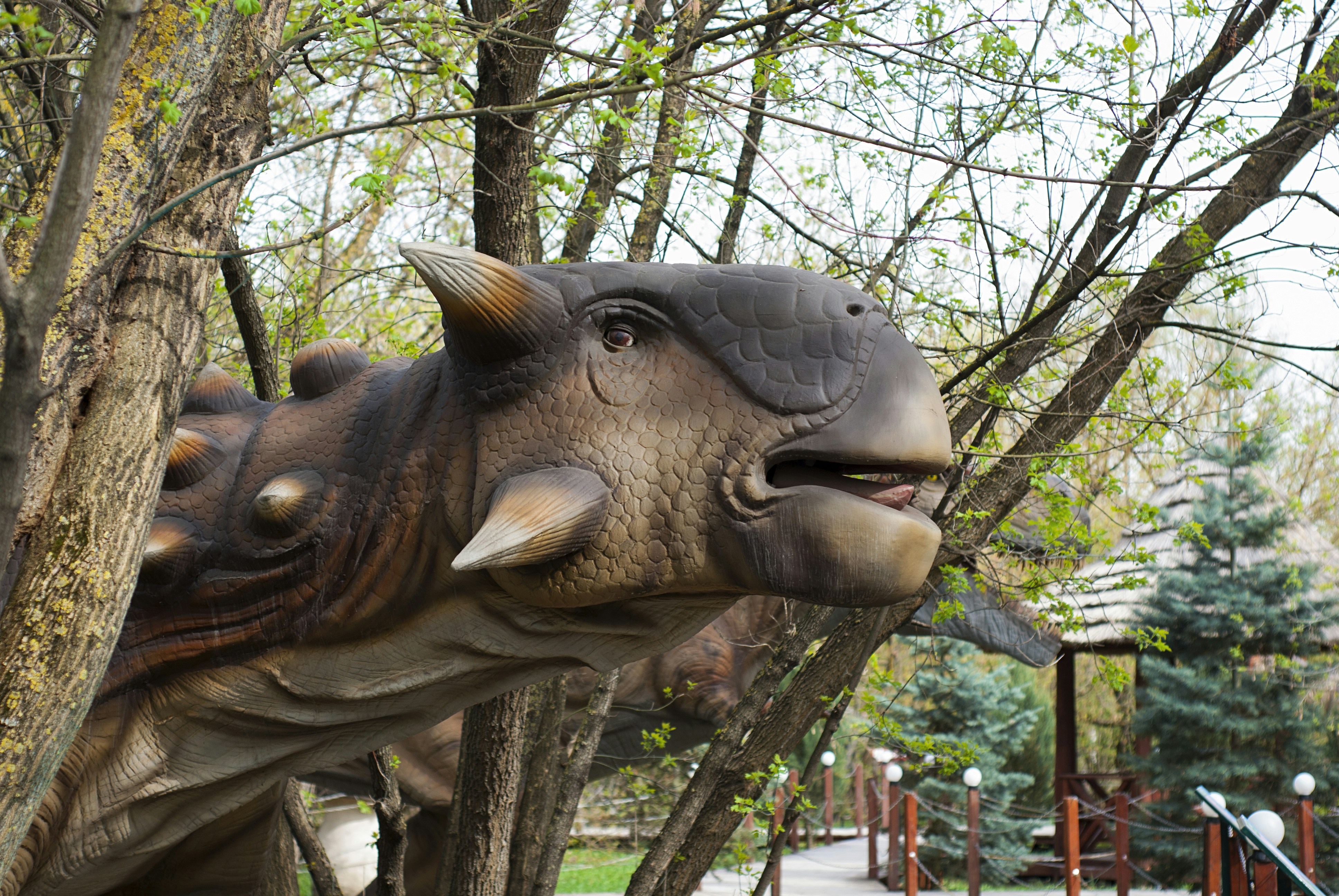 Sunlit Sentinel: A Life-Size Dinosaur Statue Nestled Among Park Trees