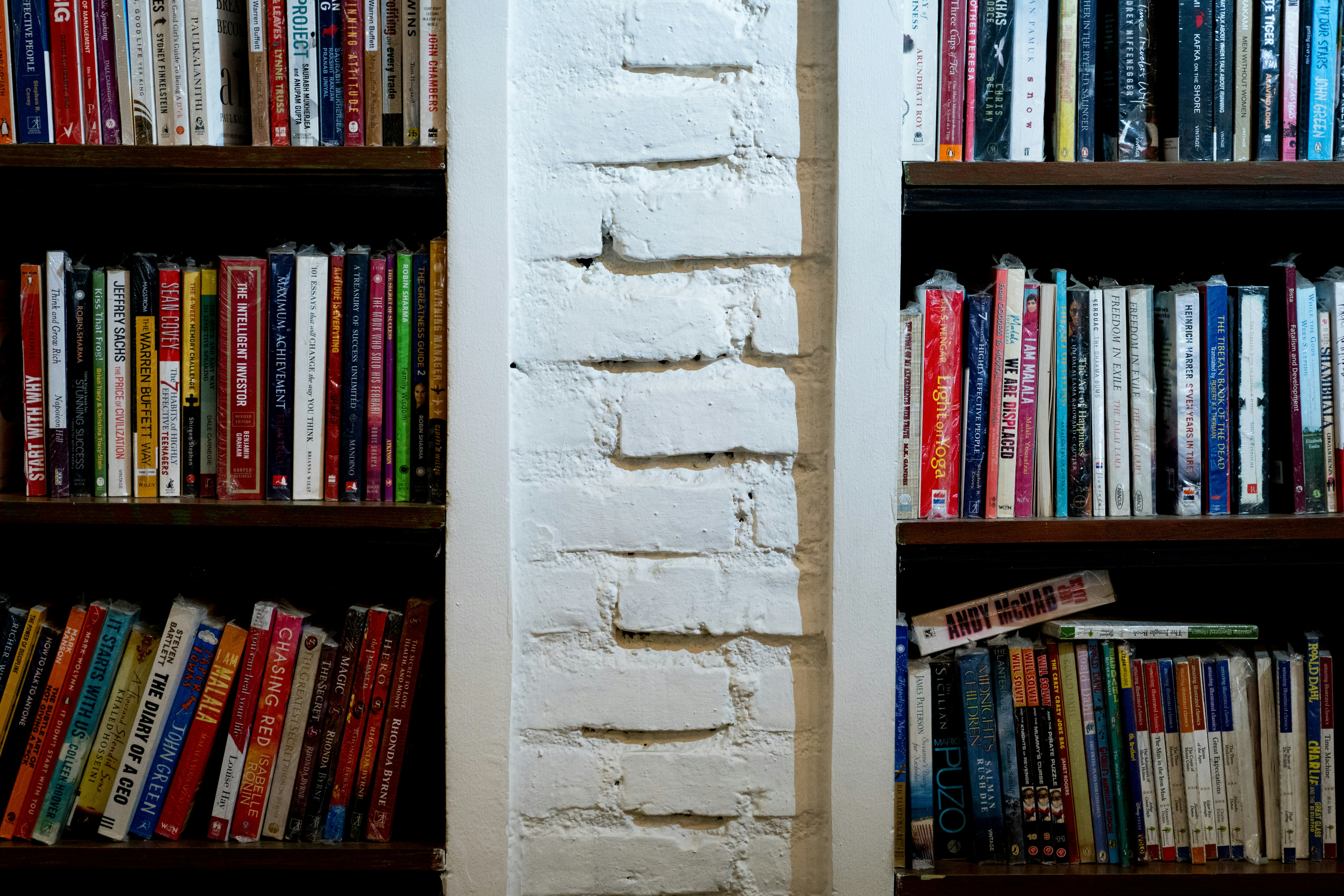 A bookshelf filled with lots of books next to a white brick wall photo ...