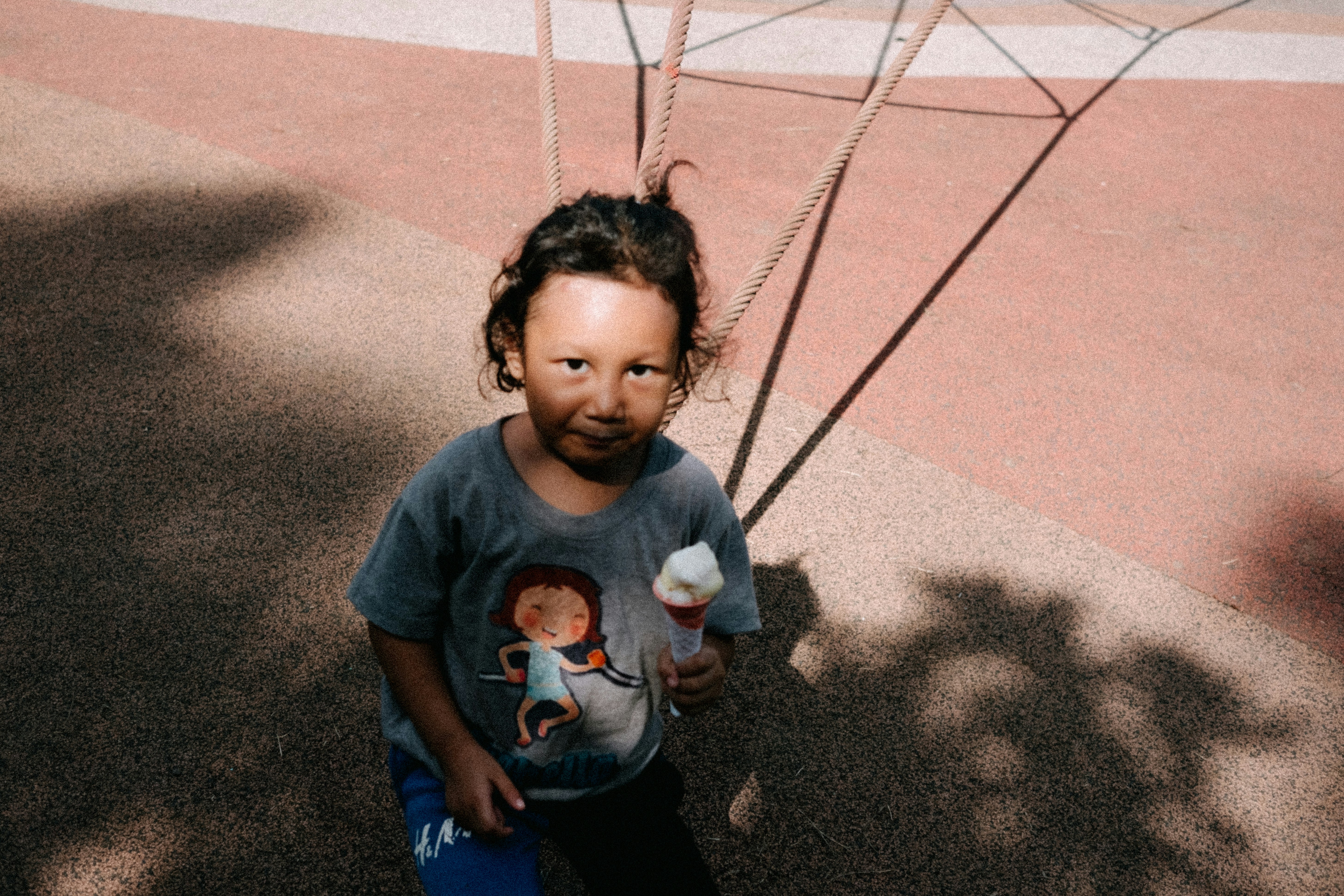 Swinging into Summer: A Curious Girl with Ice Cream Under Shaded Light