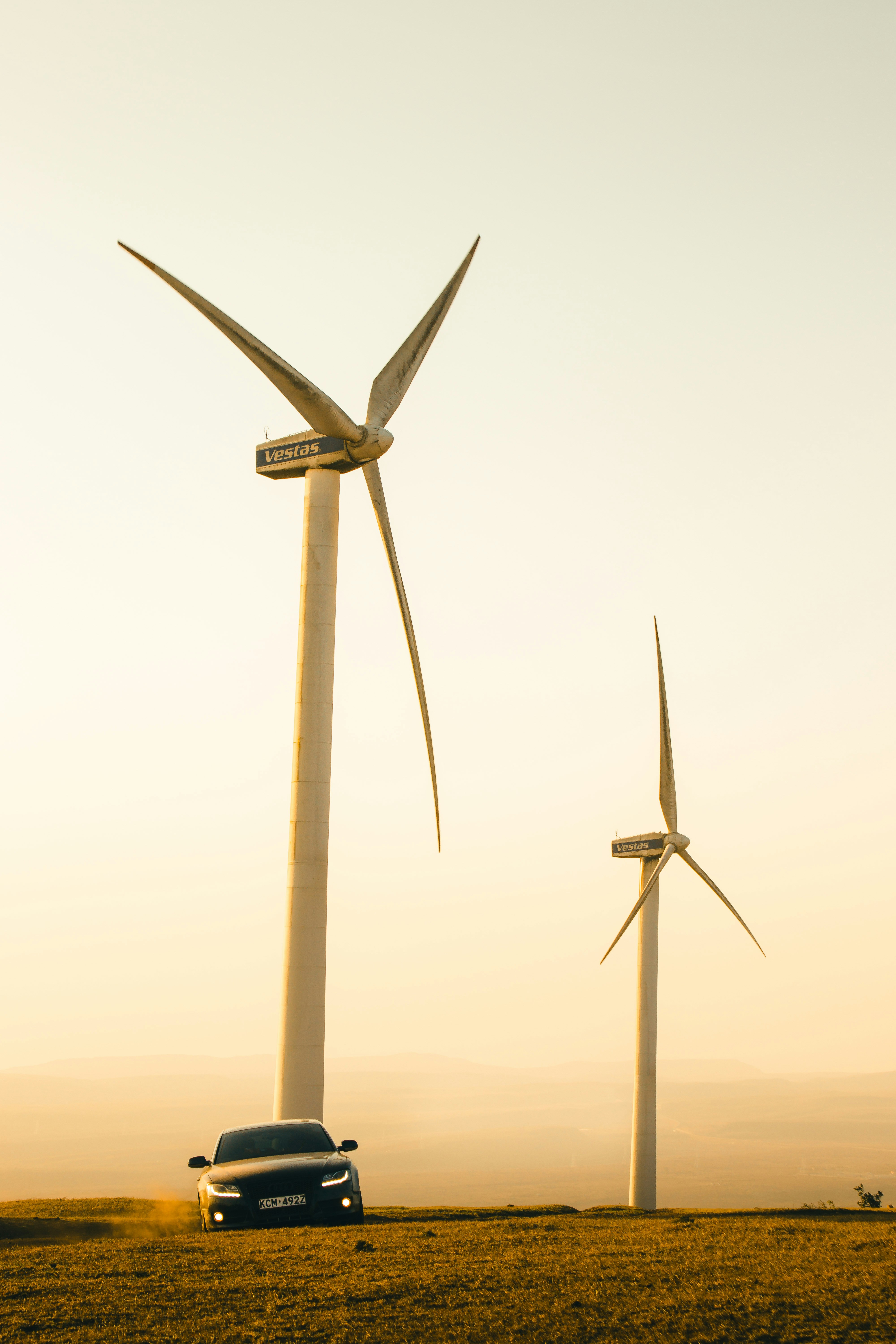 Golden Hour Sentinels: Wind Turbines and a Car on a Dusk-Soft Hill