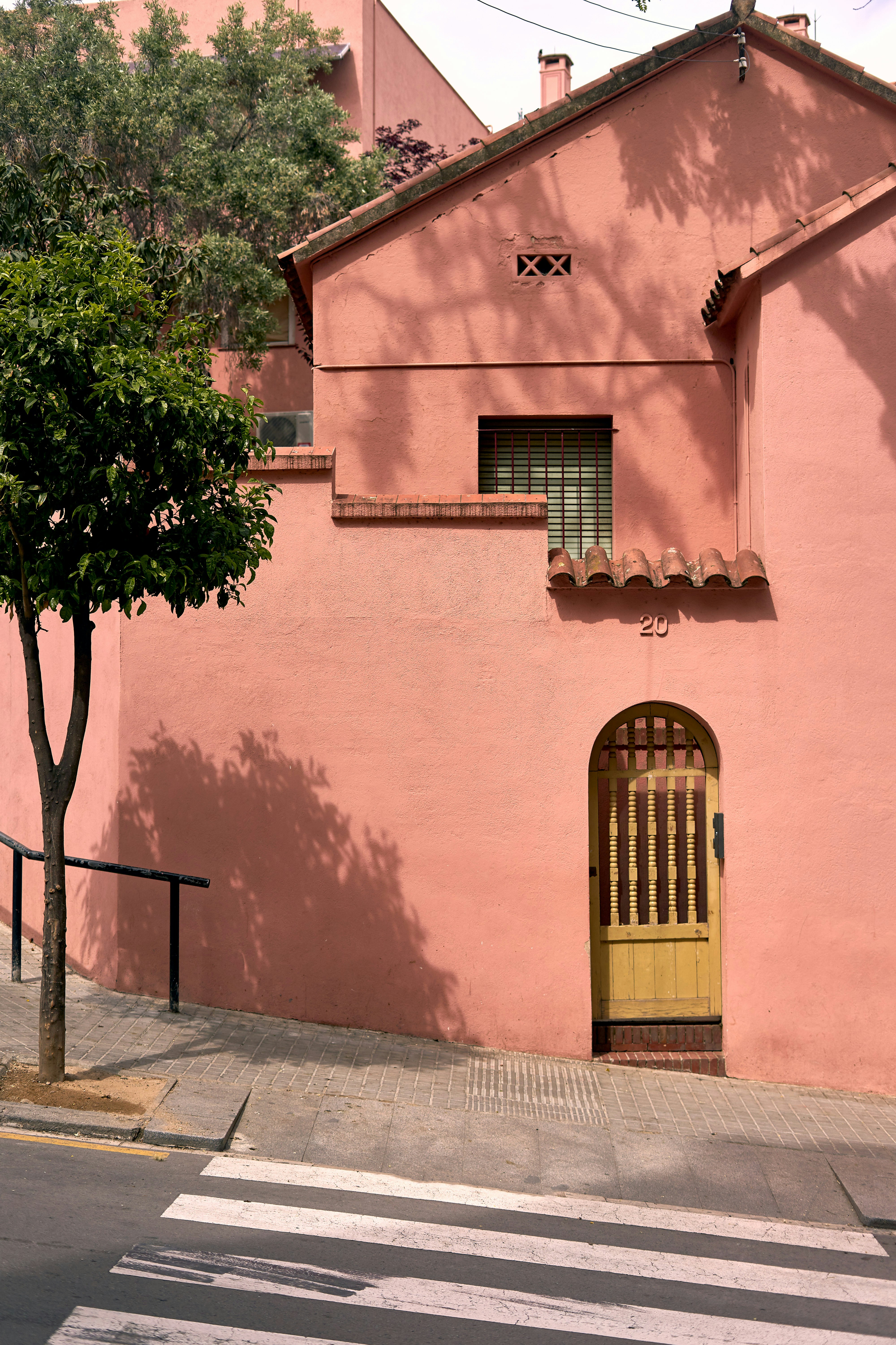 Sunlit Pink Facade with Arched Yellow Door by a Quiet Crosswalk