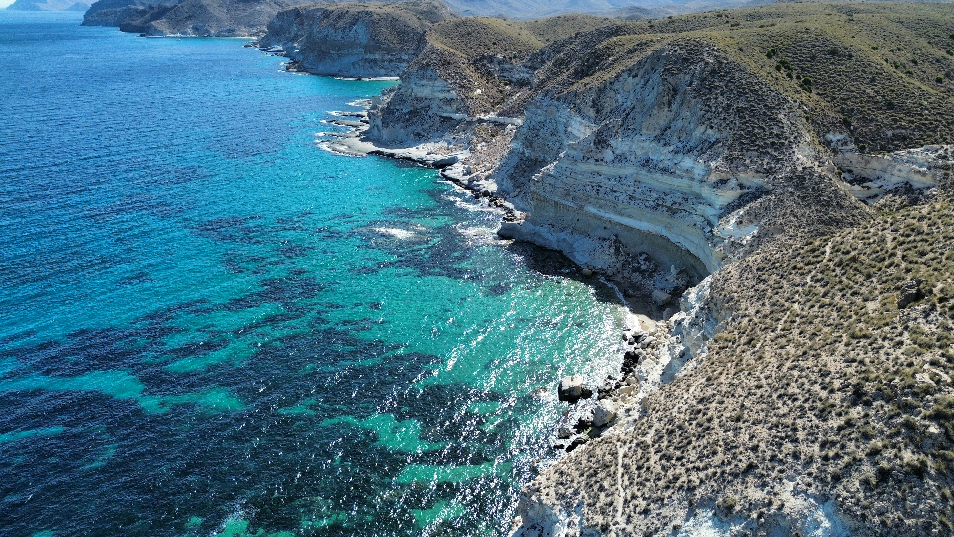 Rocky cliffs meet the vibrant turquoise sea along a remote island coast.