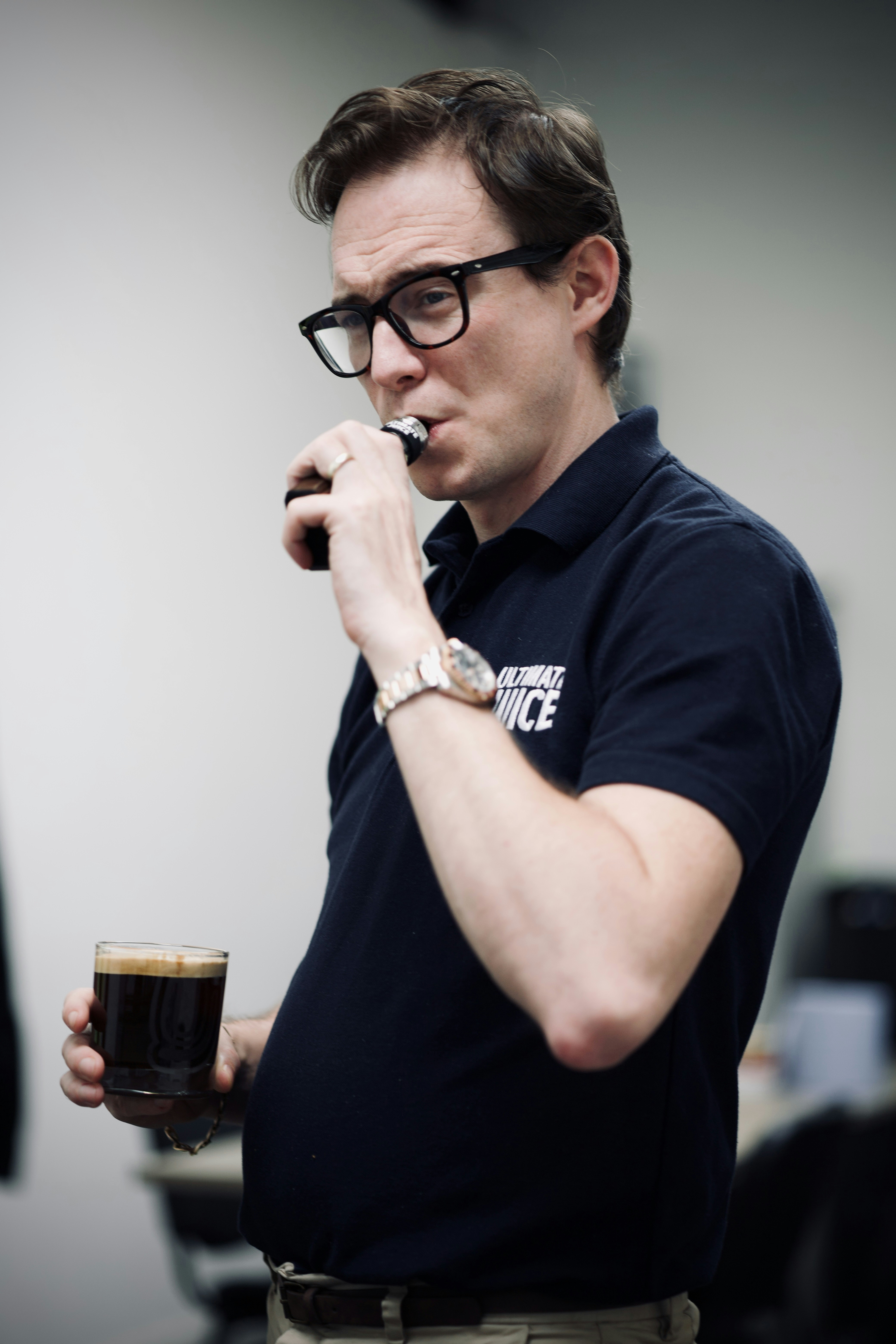 Focused Pause: Portrait of a man in a navy polo savoring a glass of dark beverage
