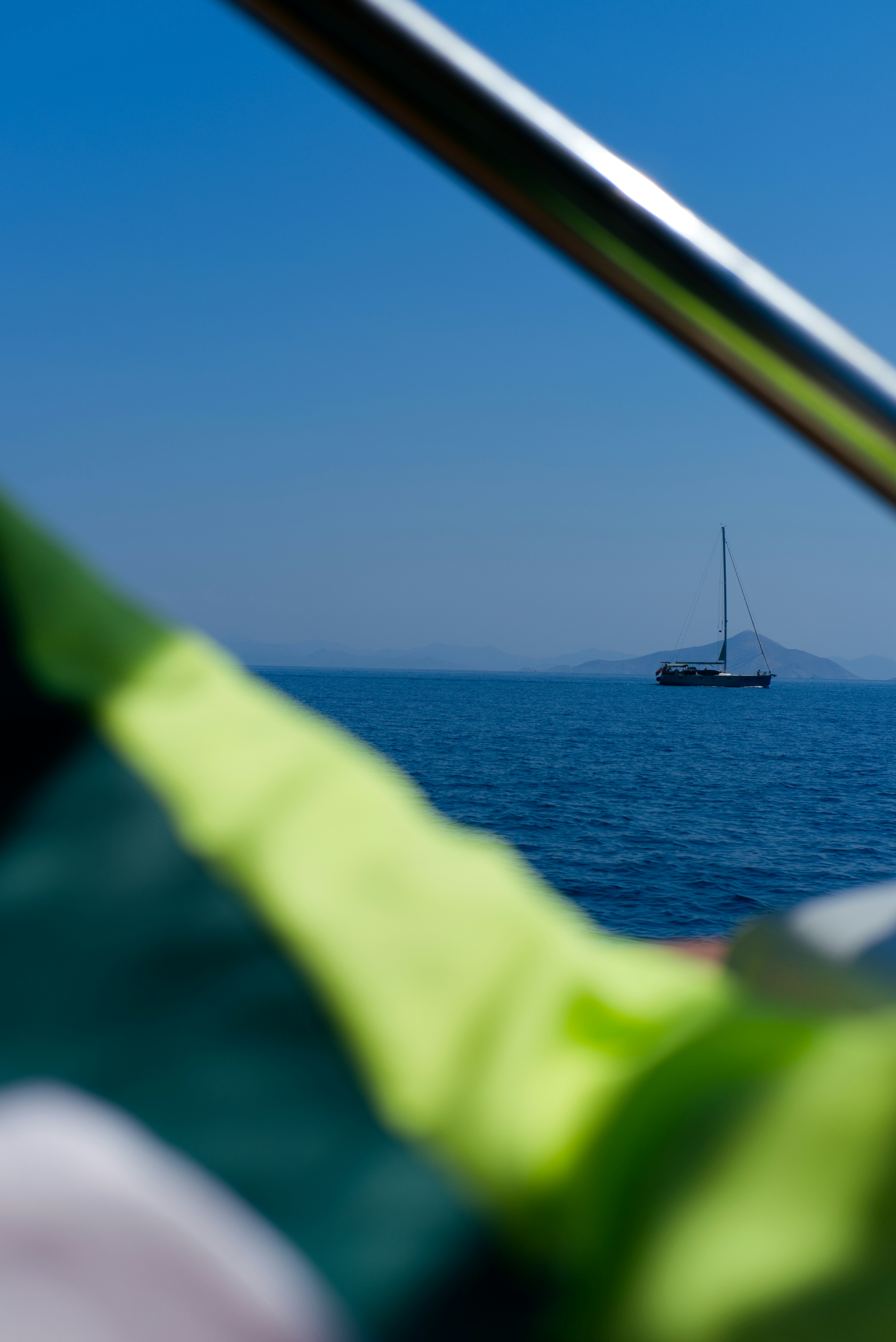 Azure Horizon: A Lone Sailboat Framed by Neon Fabric and Chrome Rail
