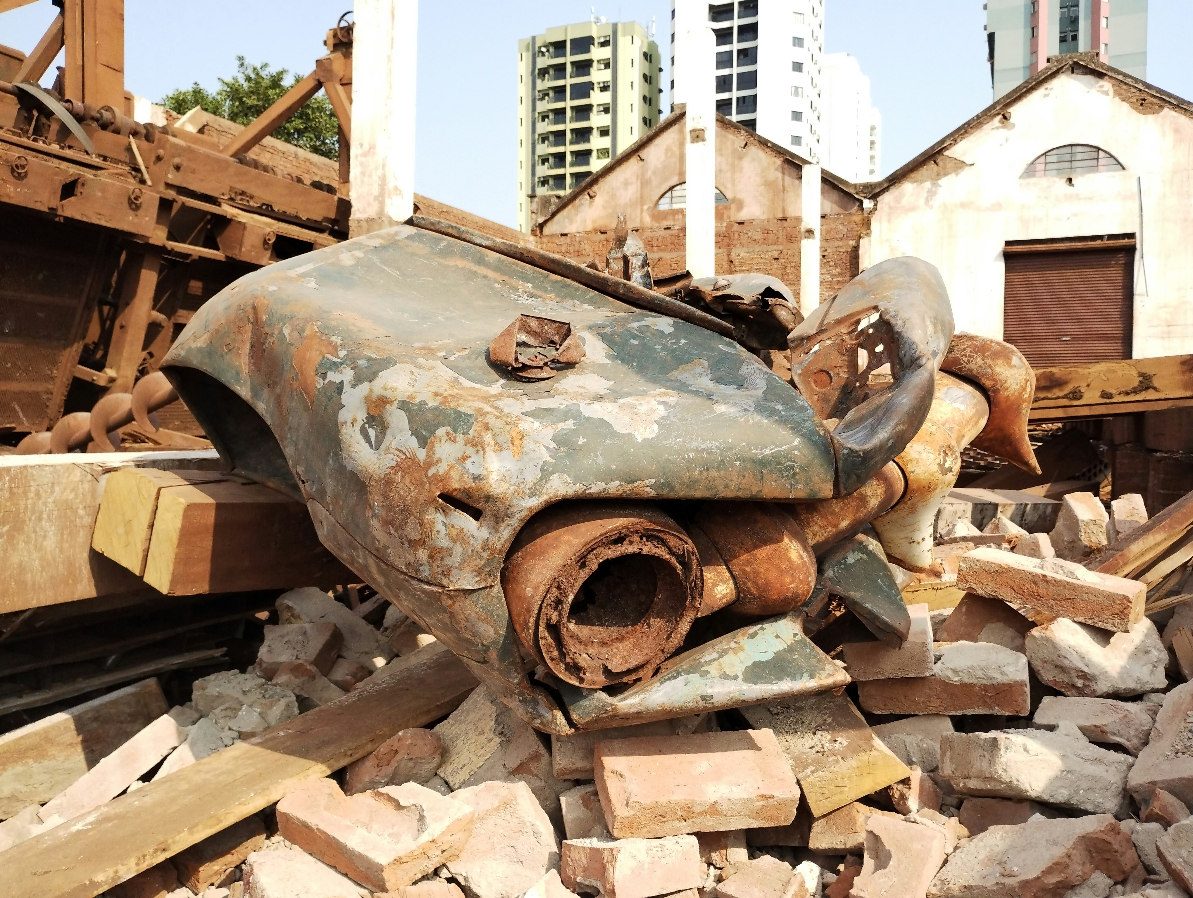 Rusted vintage car perched on rubble with modern buildings in the background.