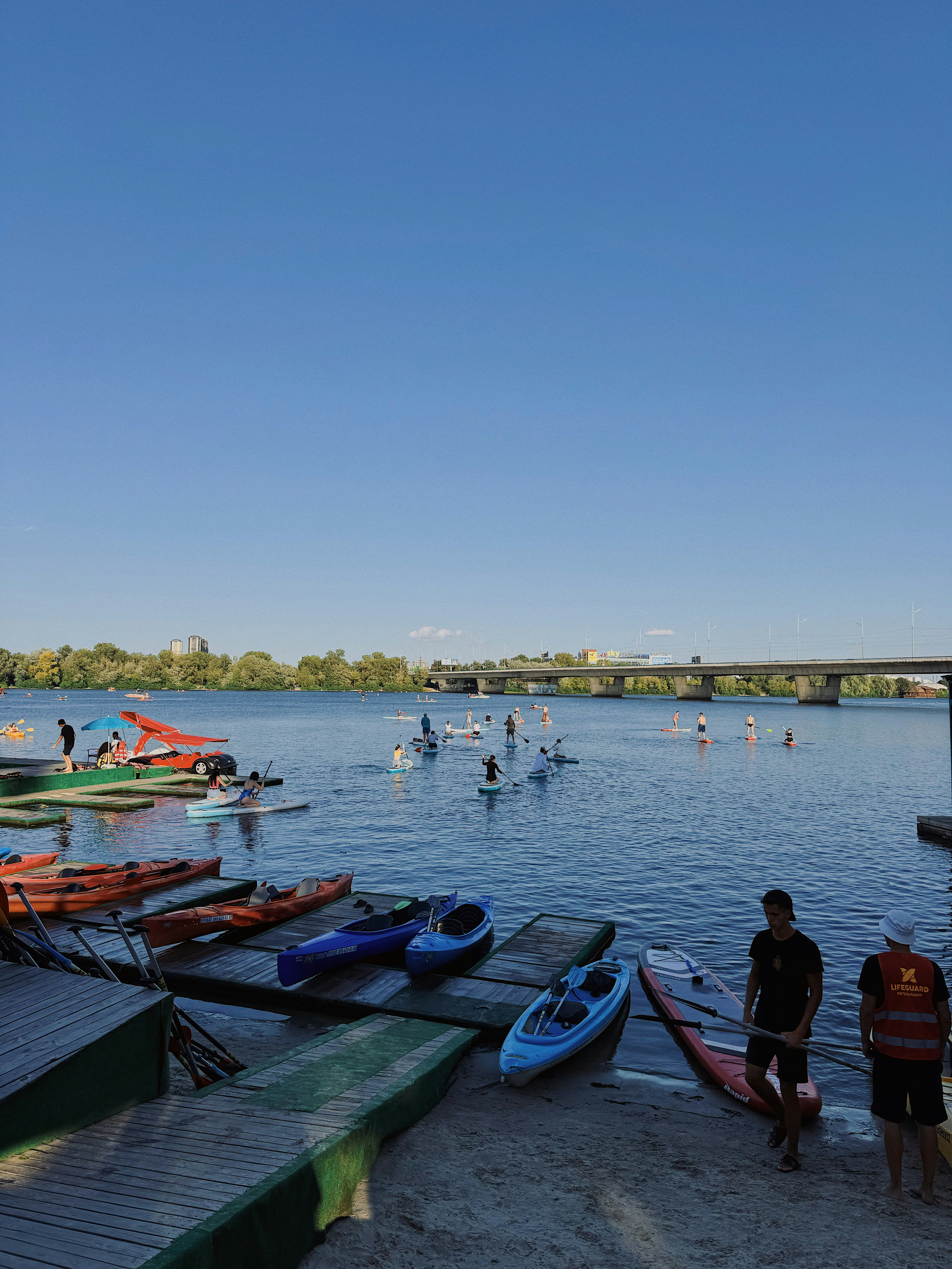 Kayakers and paddleboarders enjoying a serene day on the water, with colorful boats lined along the dock. The scene captures the essence of outdoor leisure.