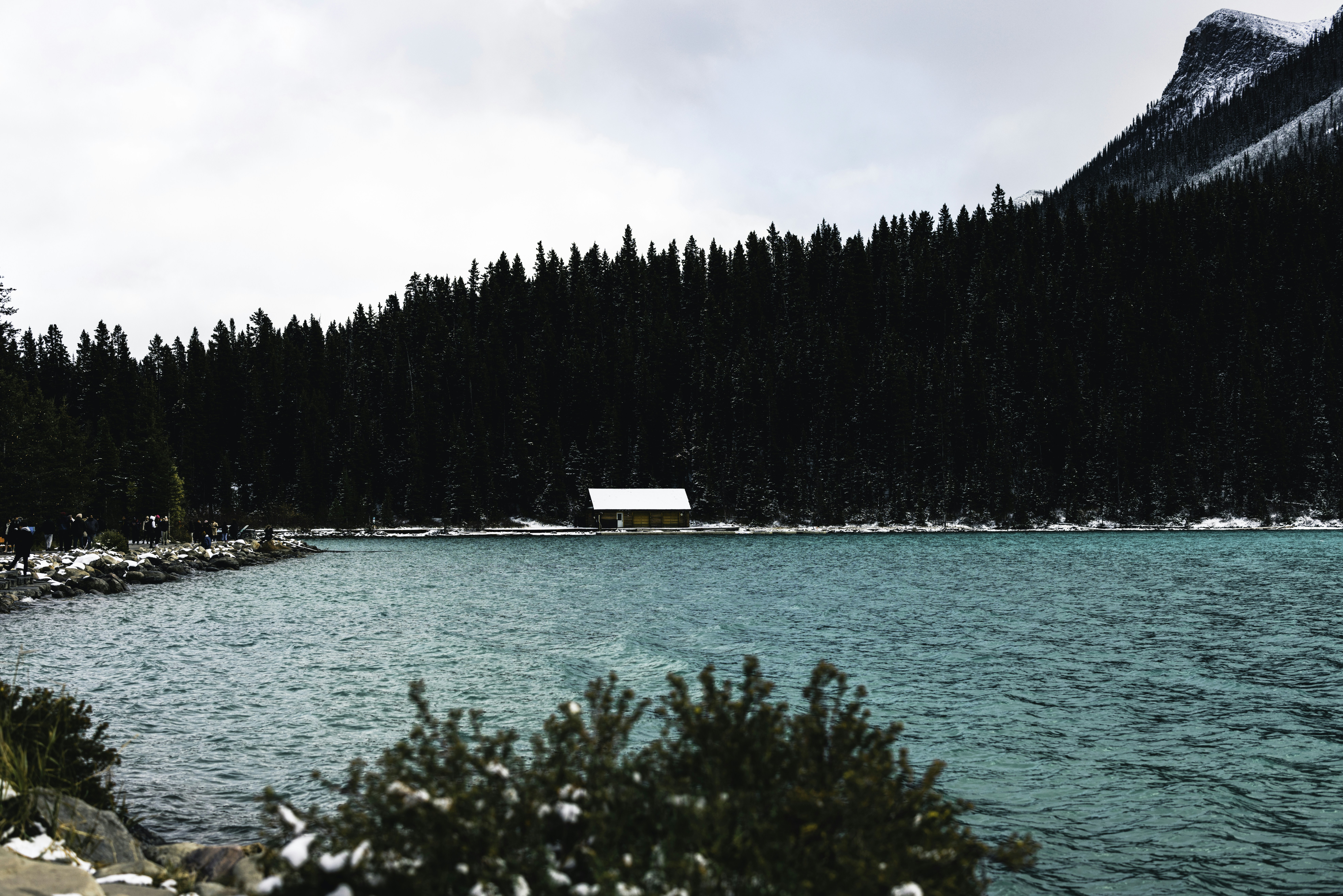 White Boathouse on a Turquoise Lake, Framed by Pines and Snowy Peaks