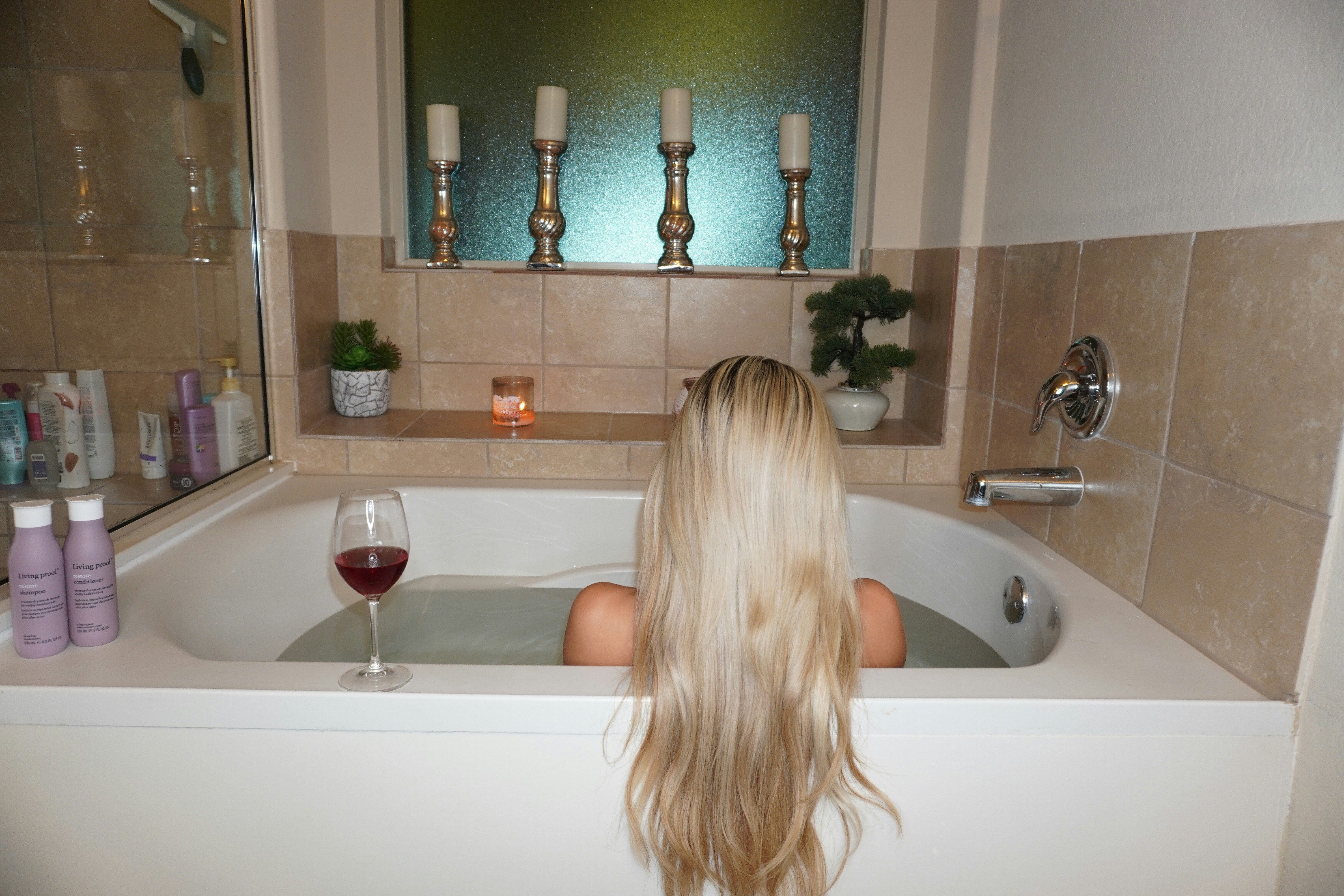 blonde woman self-care | A woman sitting in a bathtub with a glass of wine