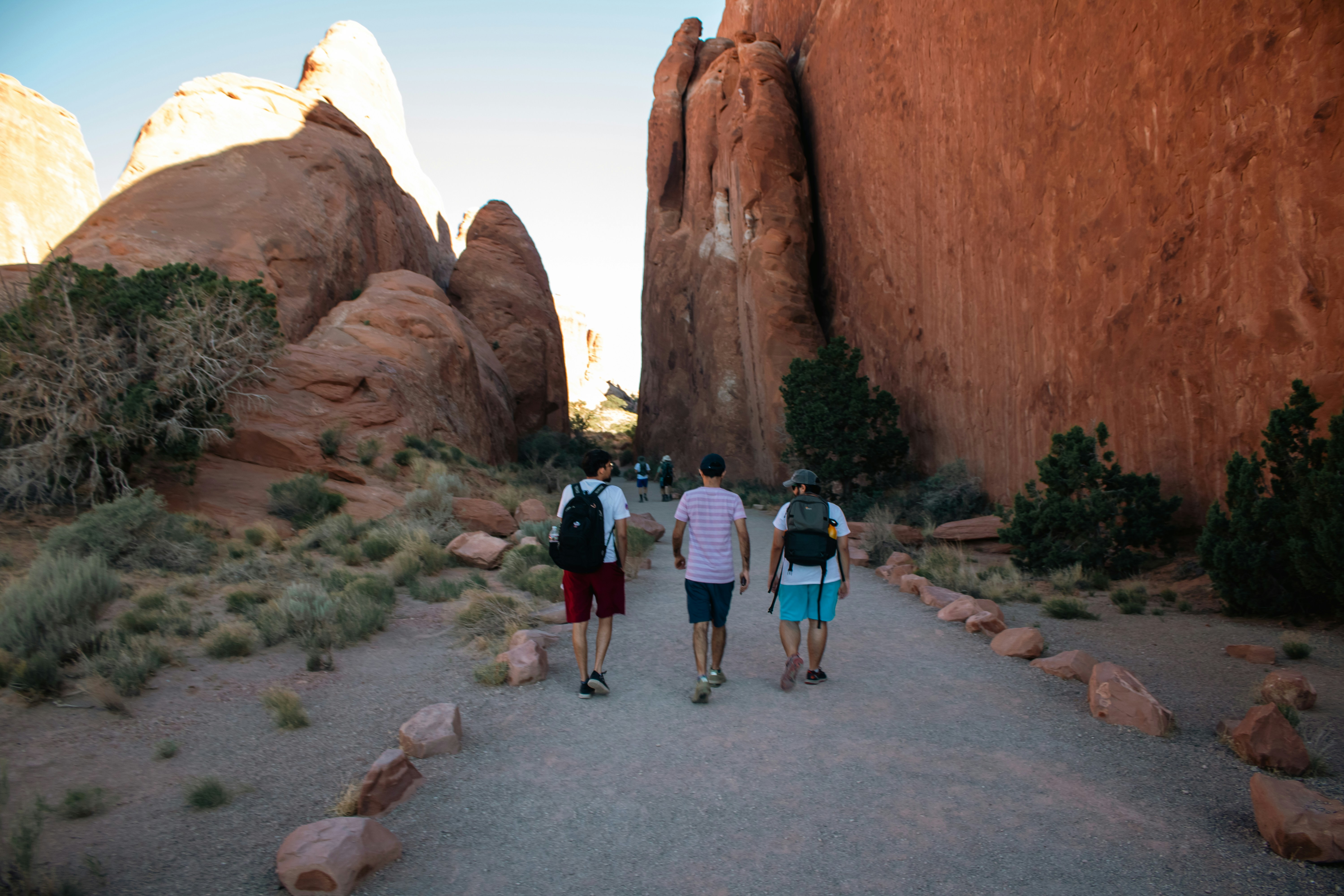 Three Hikers Tread a Desert Corridor Between Weathered Red Rocks