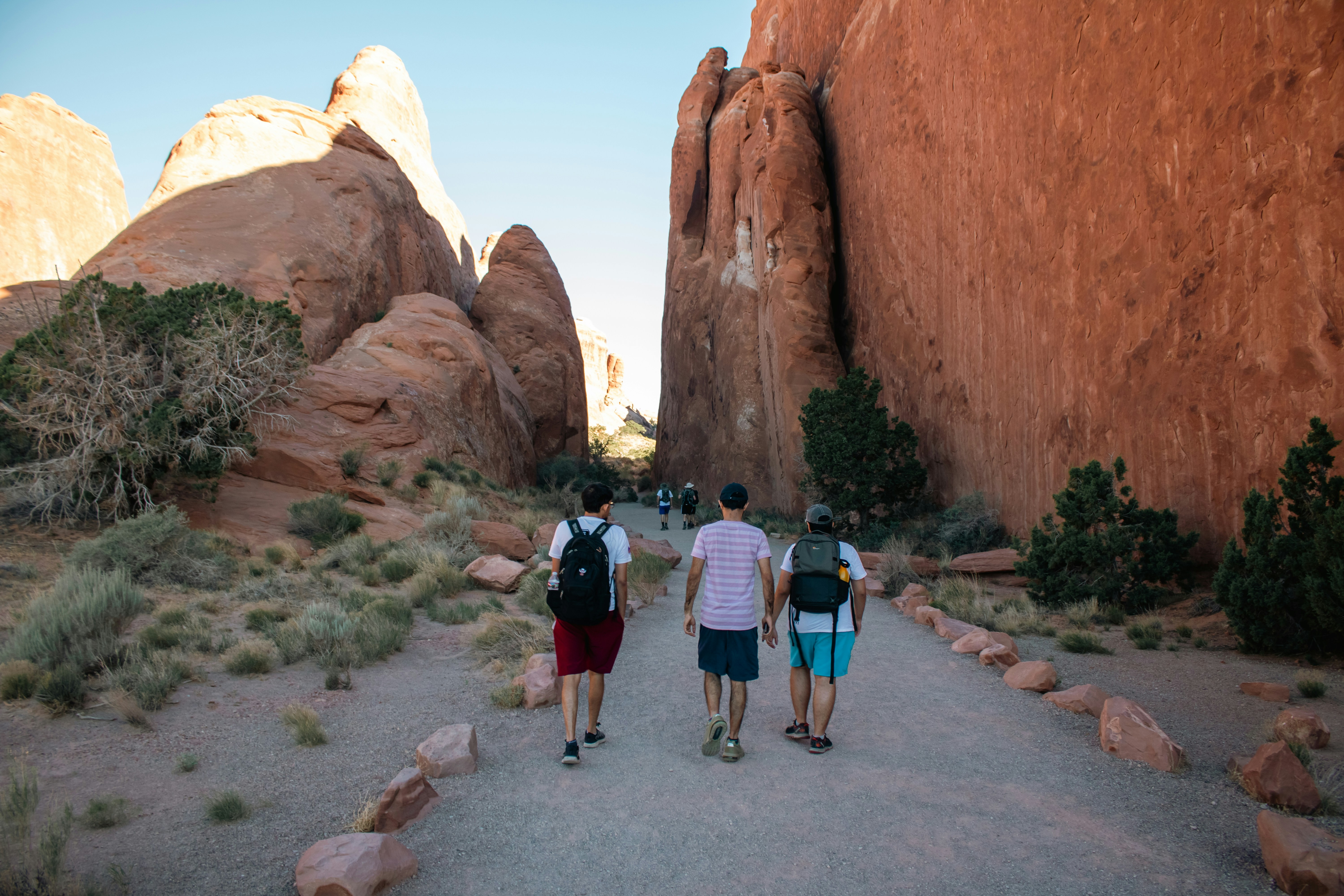 Three Explorers Navigate a Rust-Red Canyon Path