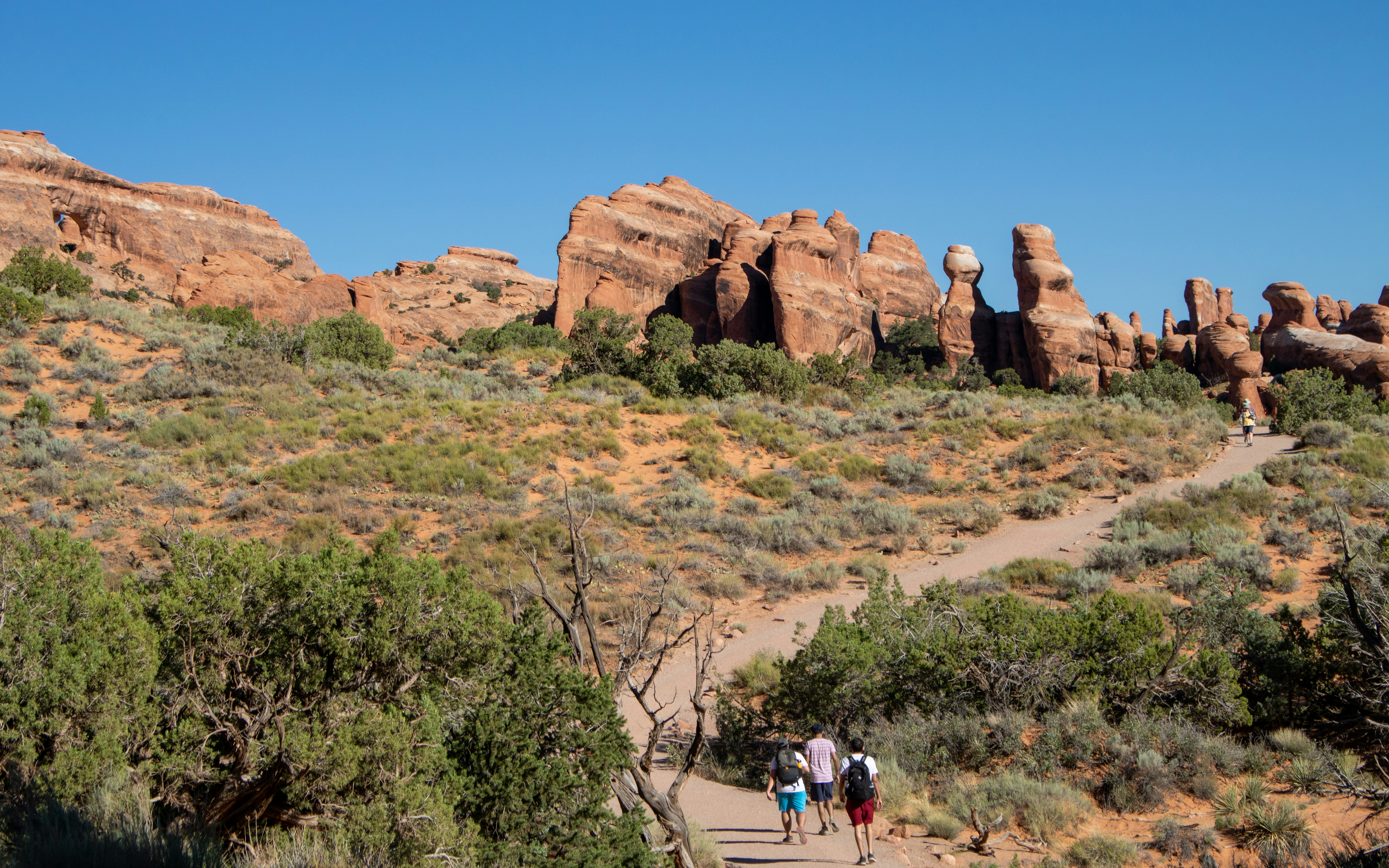 A group of friends walking on a dirt trail path in Devils Garden, Arches National Park, Utah, USA.