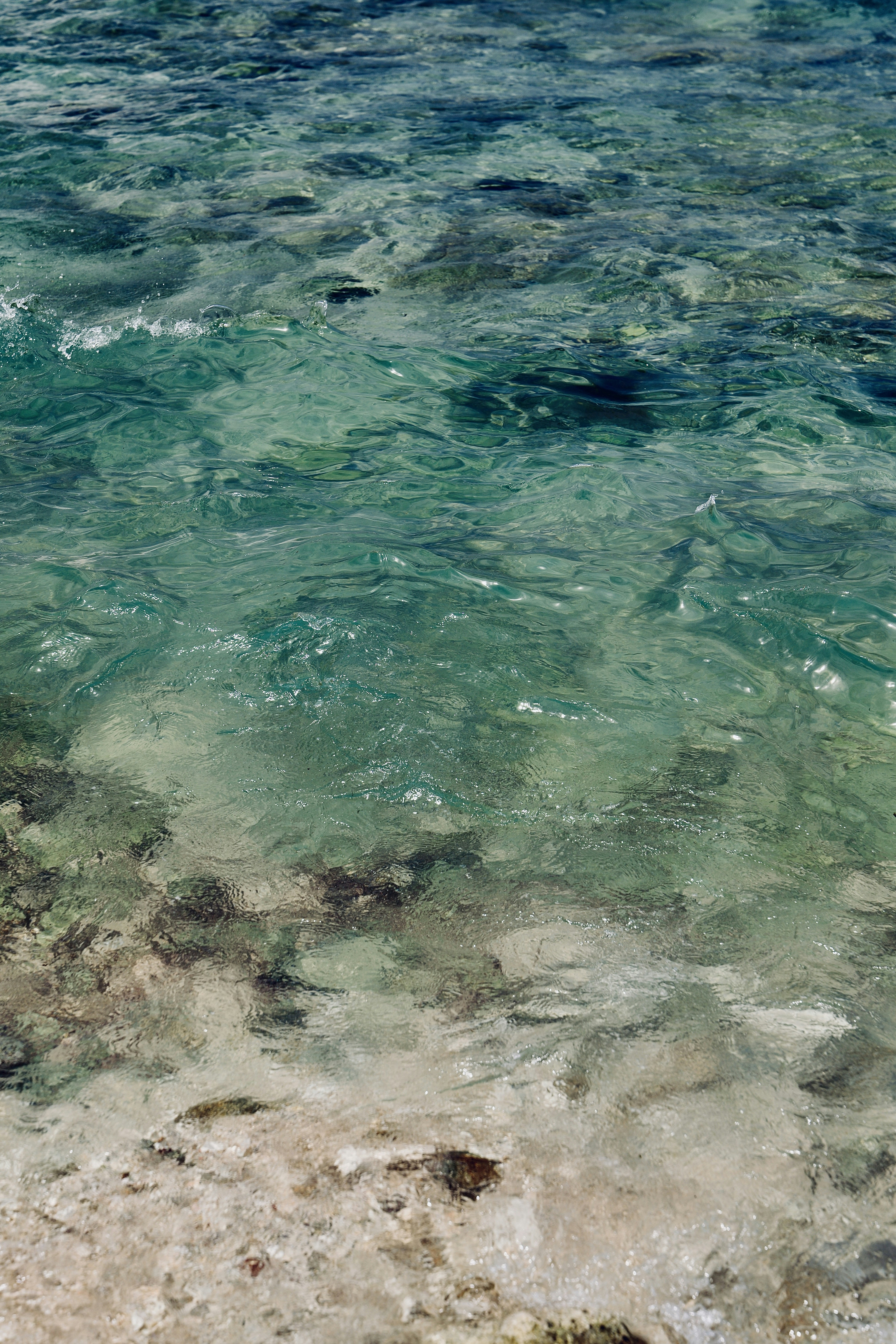 A close-up of the clear ocean water, showcasing the intricate patterns and colors beneath the surface. | A person standing in the water with a surfboard