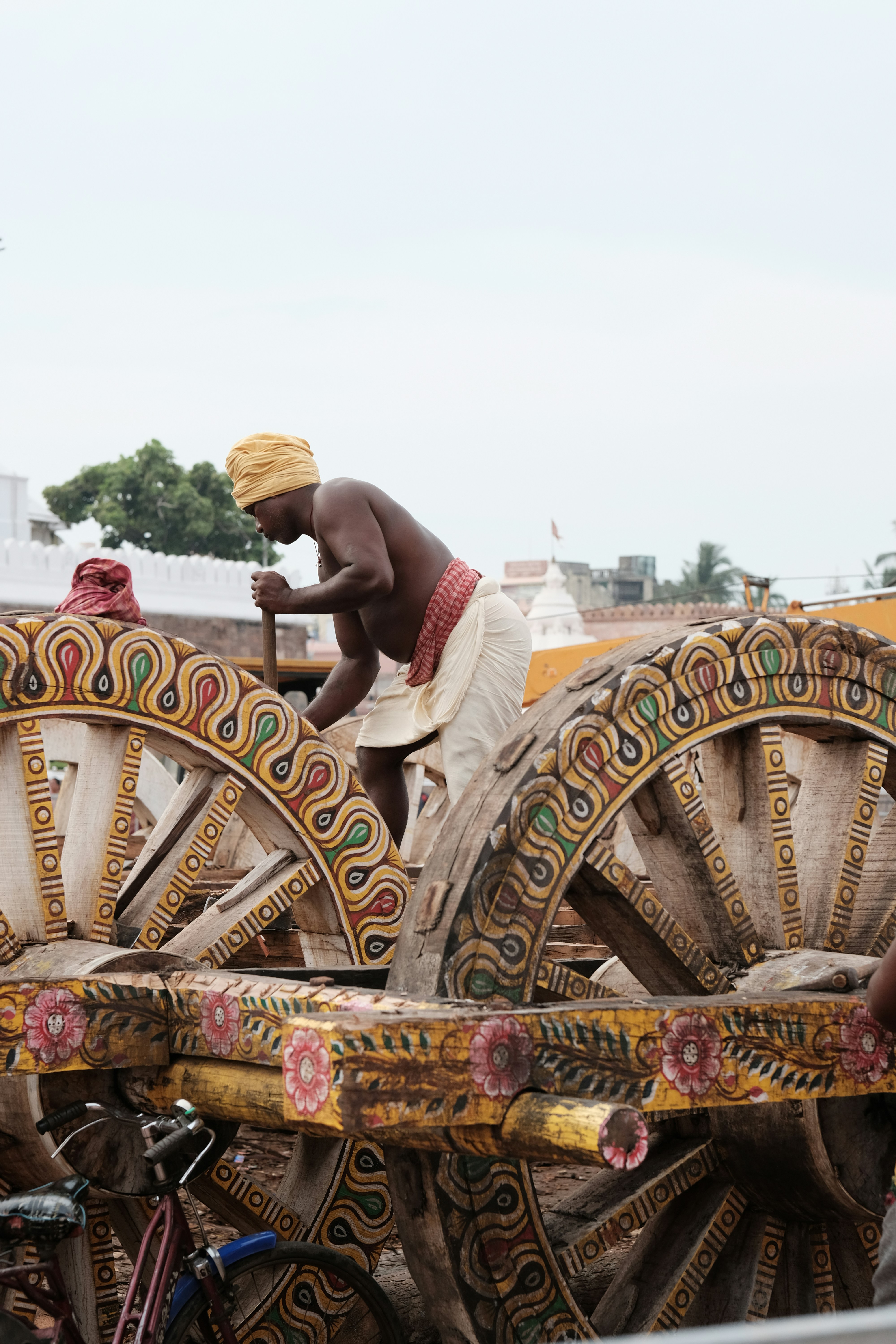 Stride Across Carved Wheels: A Turbaned Laborer Among Ornate Carriages