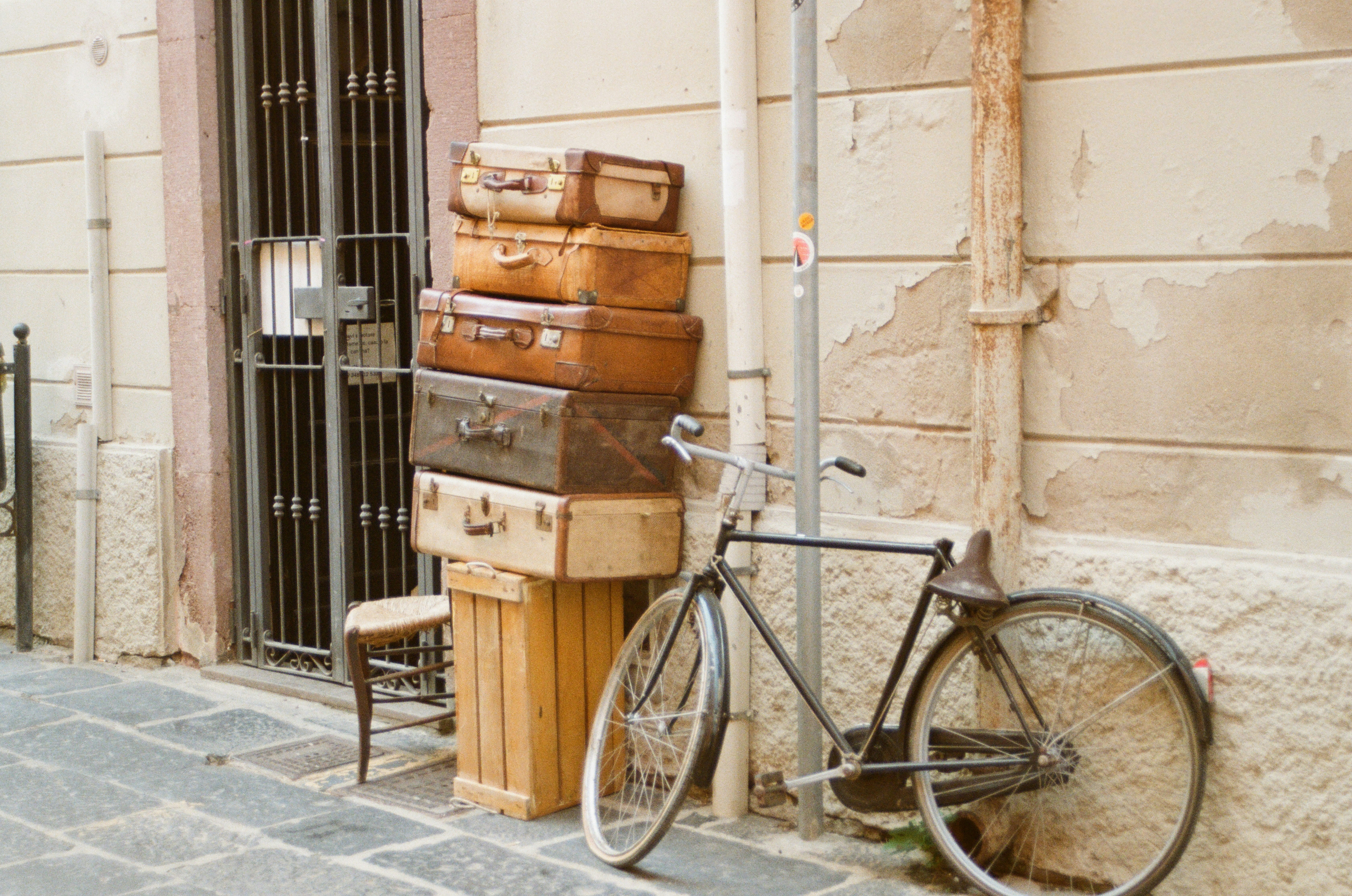 A bicycle parked next to a building with luggage stacked on top of it ...
