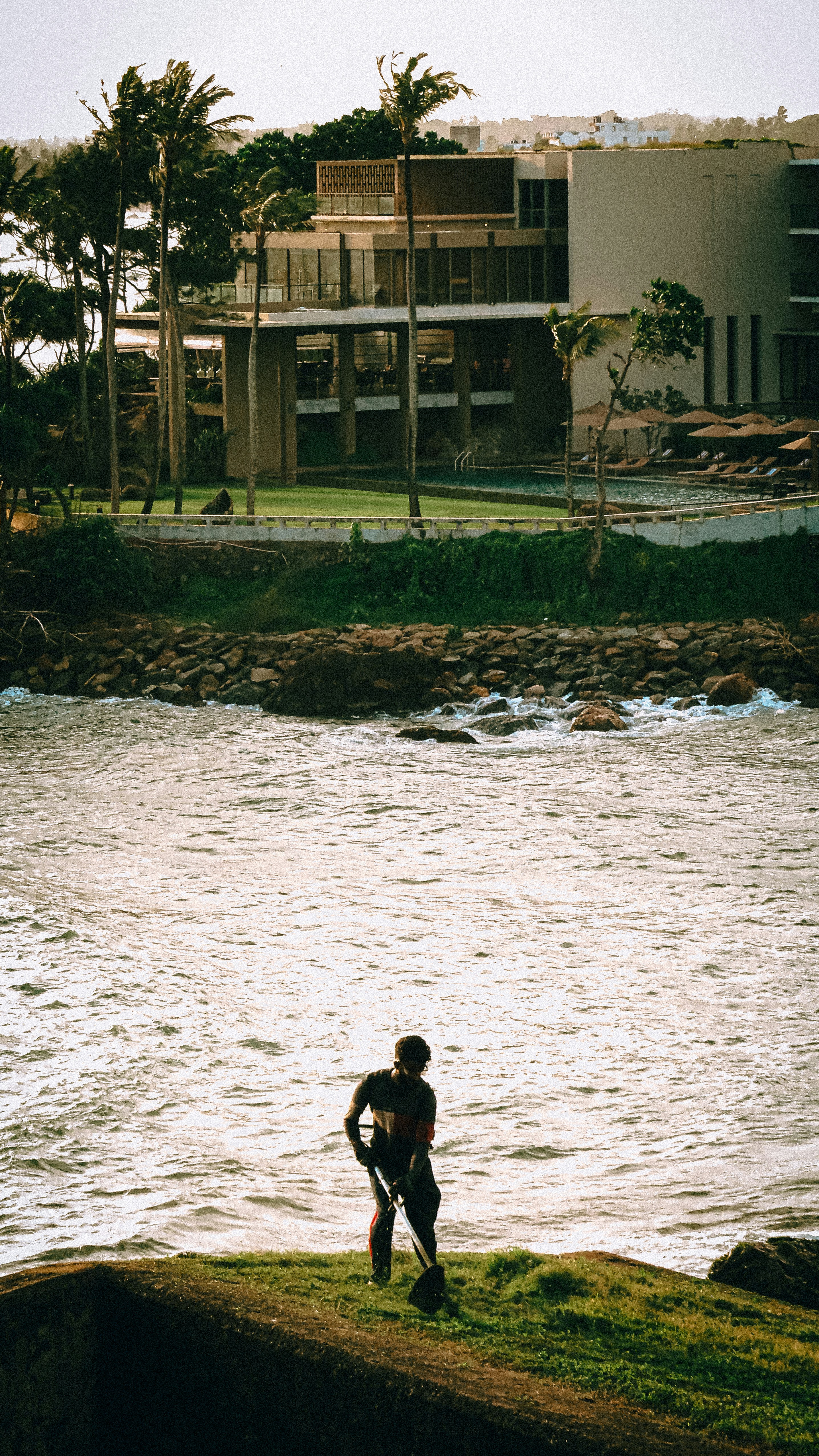 Shoreline Steward: A lone worker tends the coast as a resort rises behind palm trees