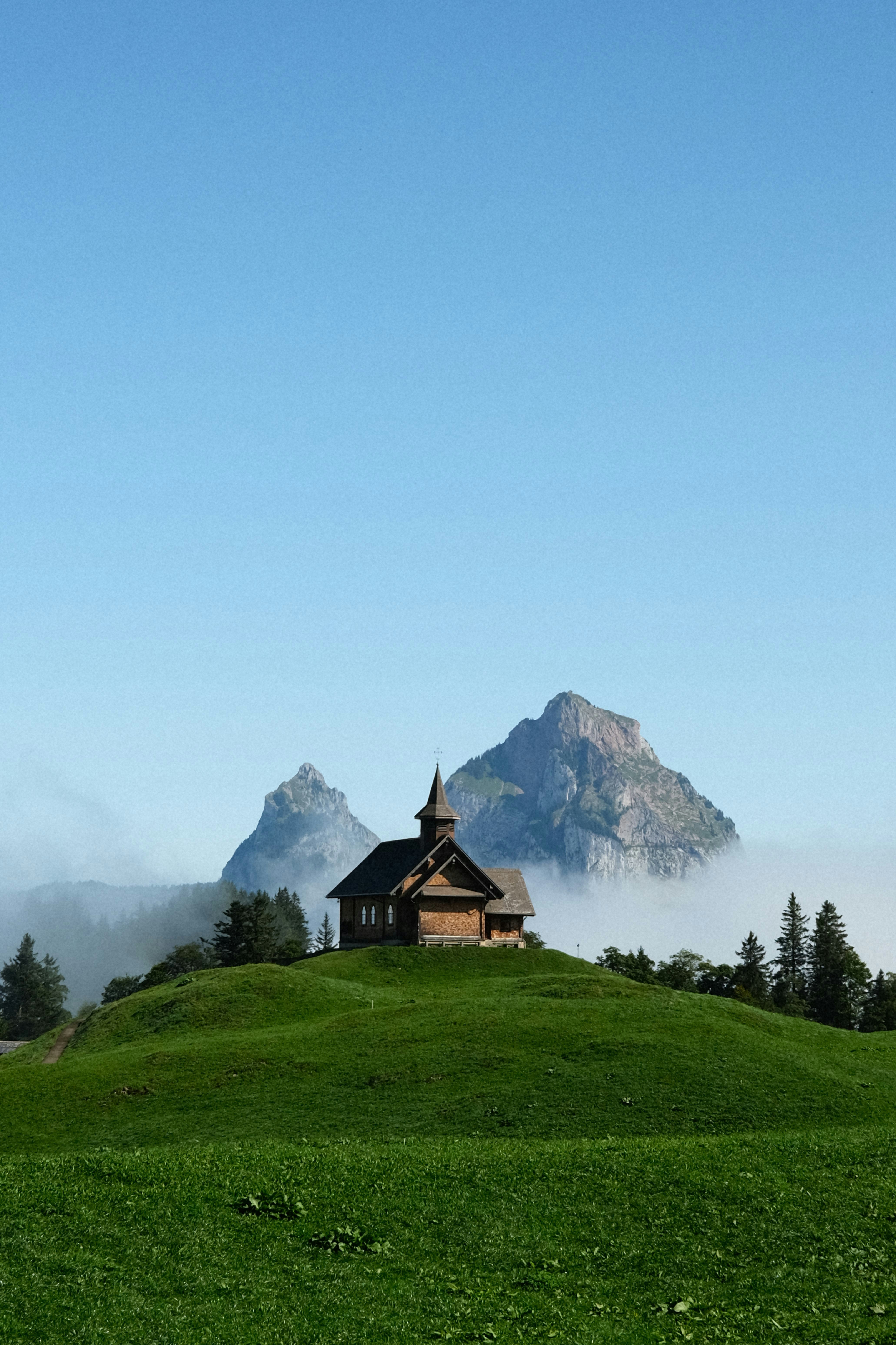 A small church on a green hill with mountains in the background photo ...