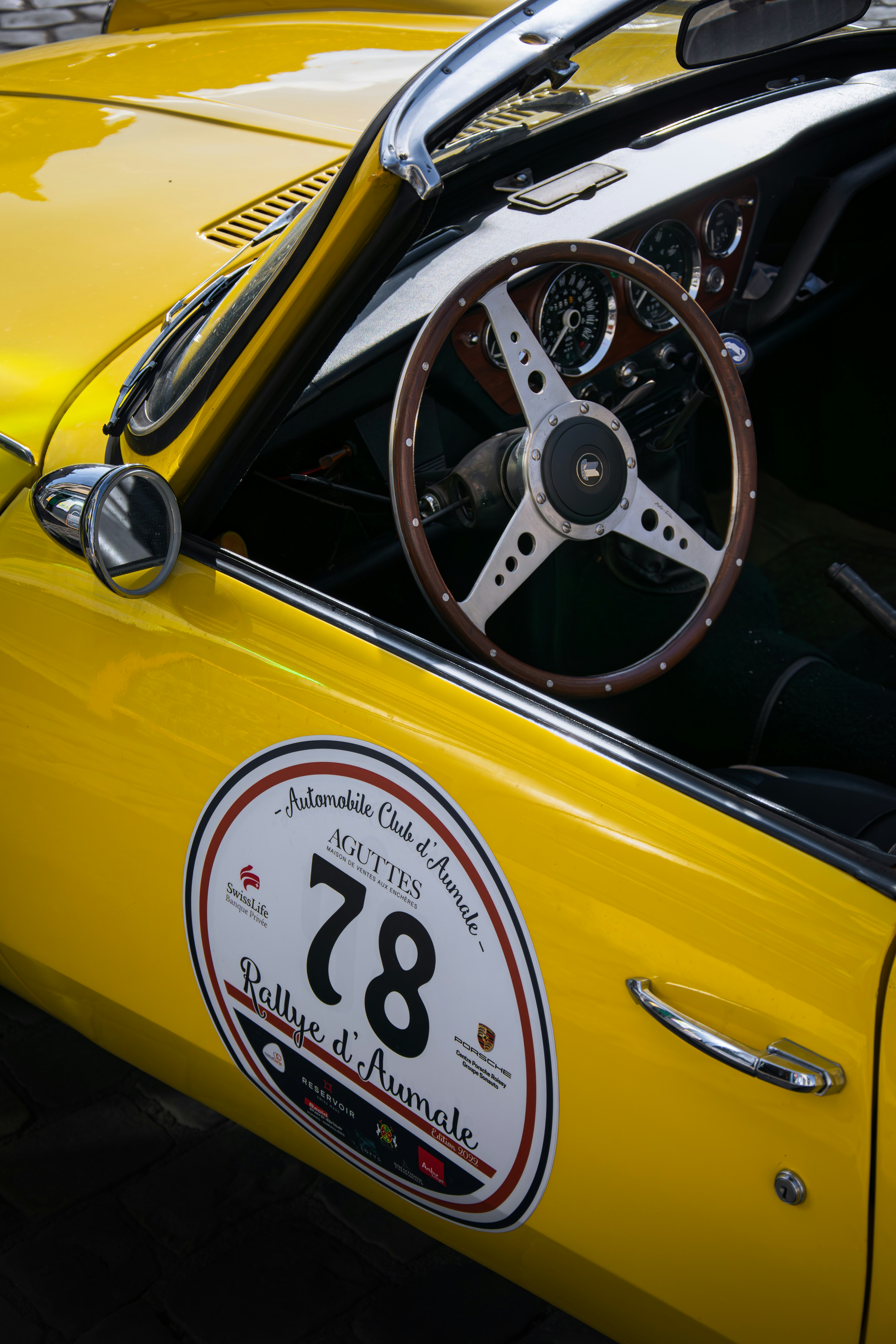 Sunlit Vintage Racer: Wooden Wheel and Rally Plate in a Yellow Cockpit