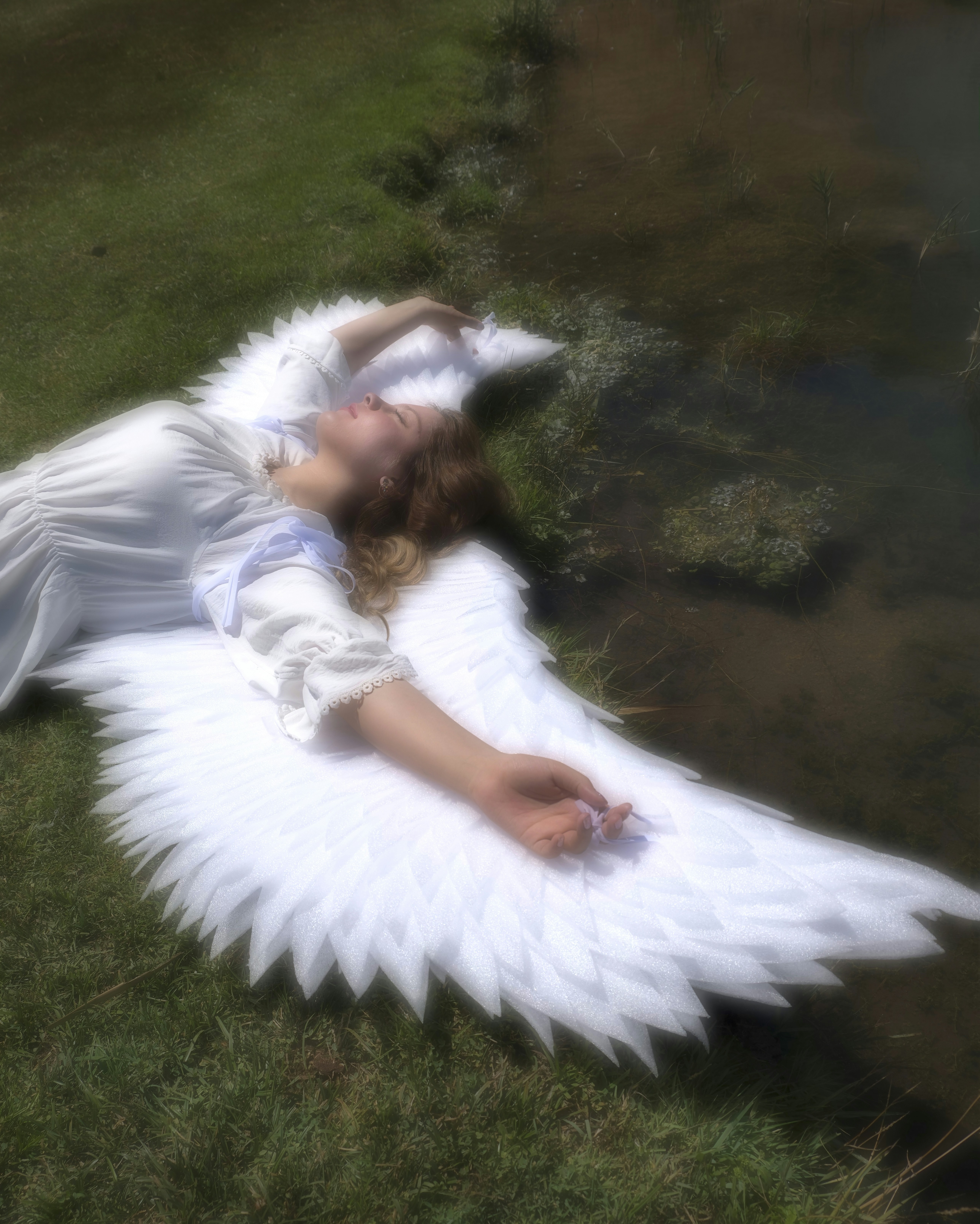 An angel laying on the ground next to a body of water photo – Free ...