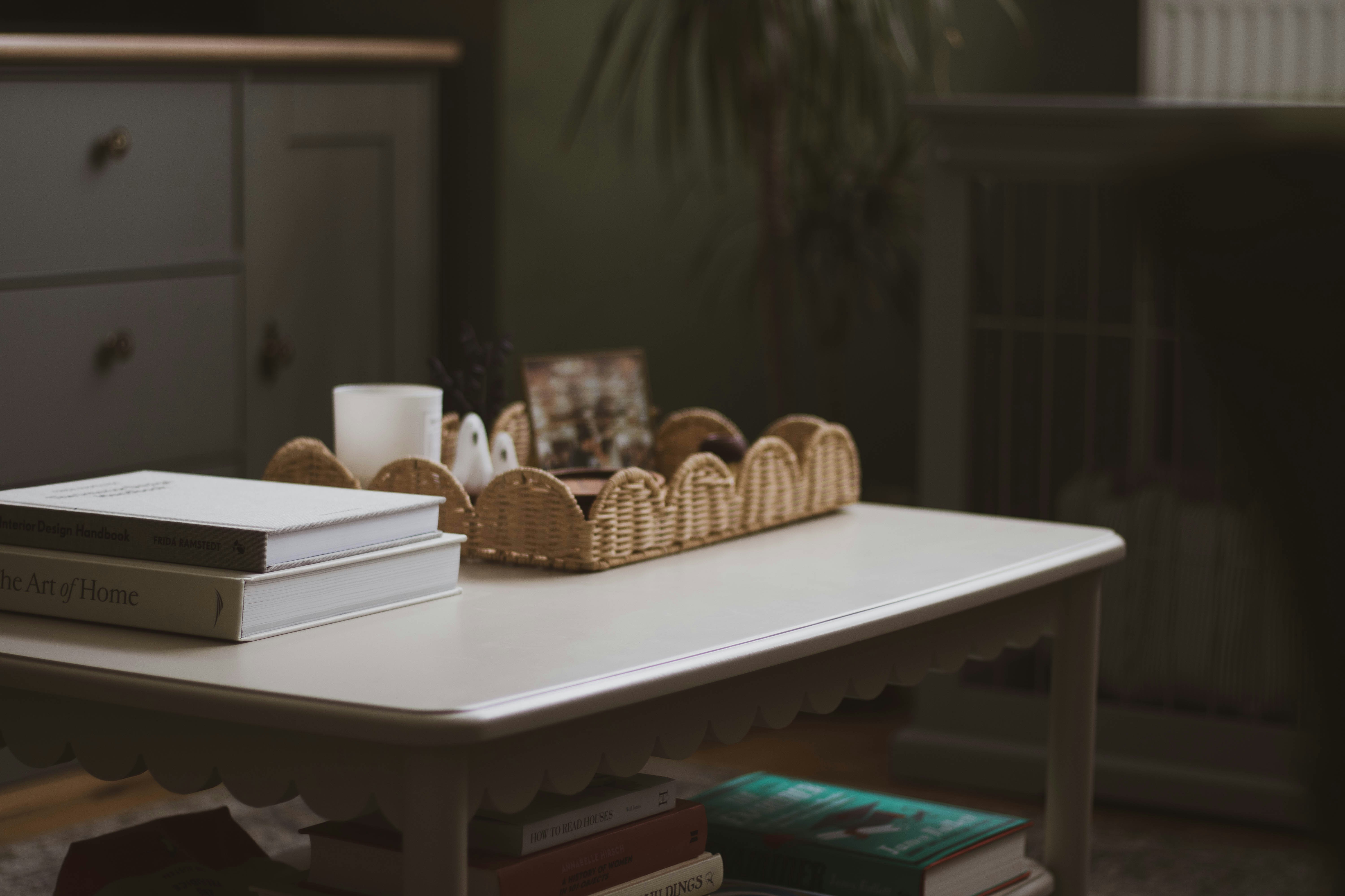 Quiet Glow on a White Coffee Table: Stacks of Books, a Wicker Tray, and a Lone Mug