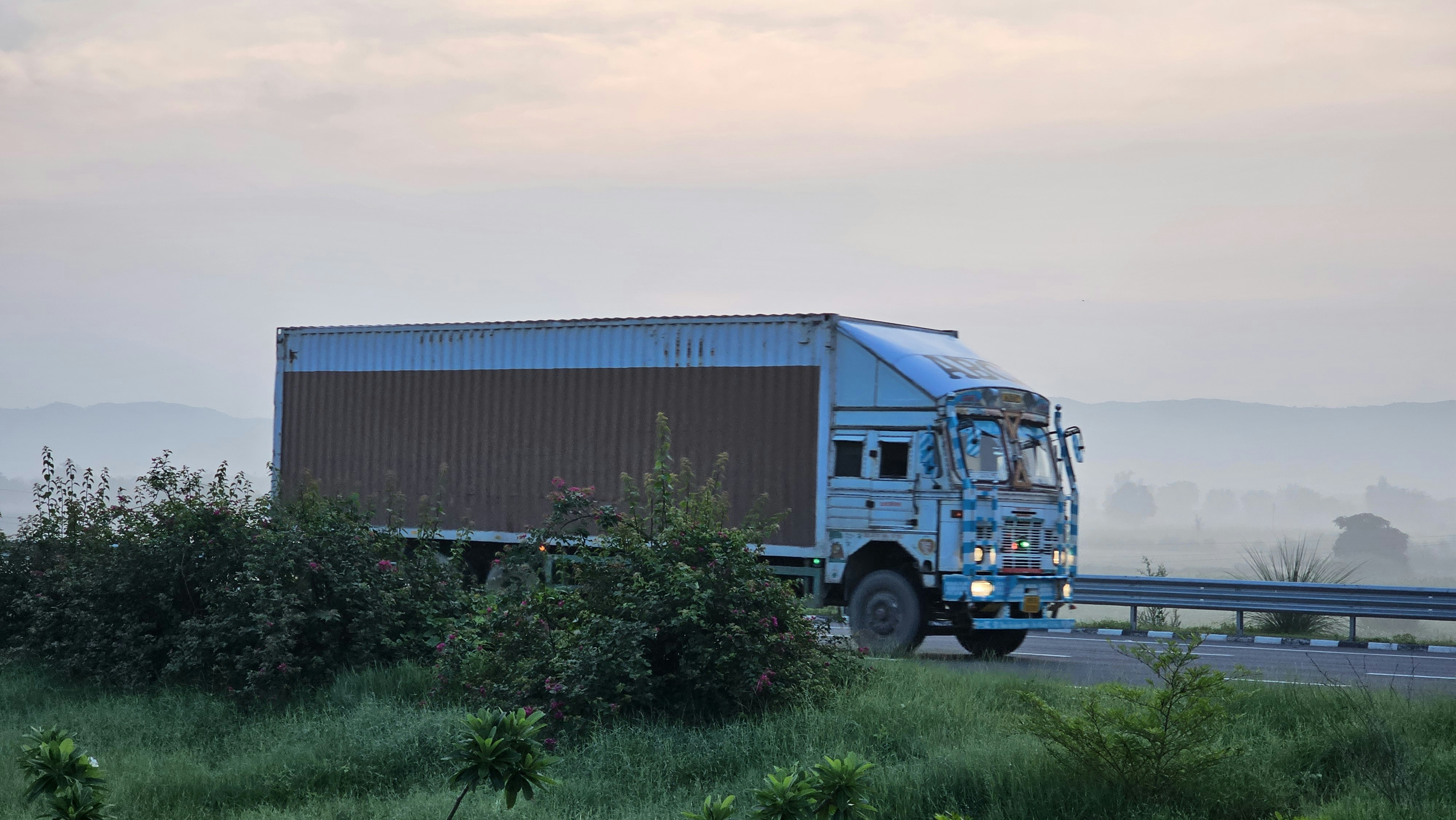 Dawn Hauler in the Mist: A Blue Truck on the Quiet Highway