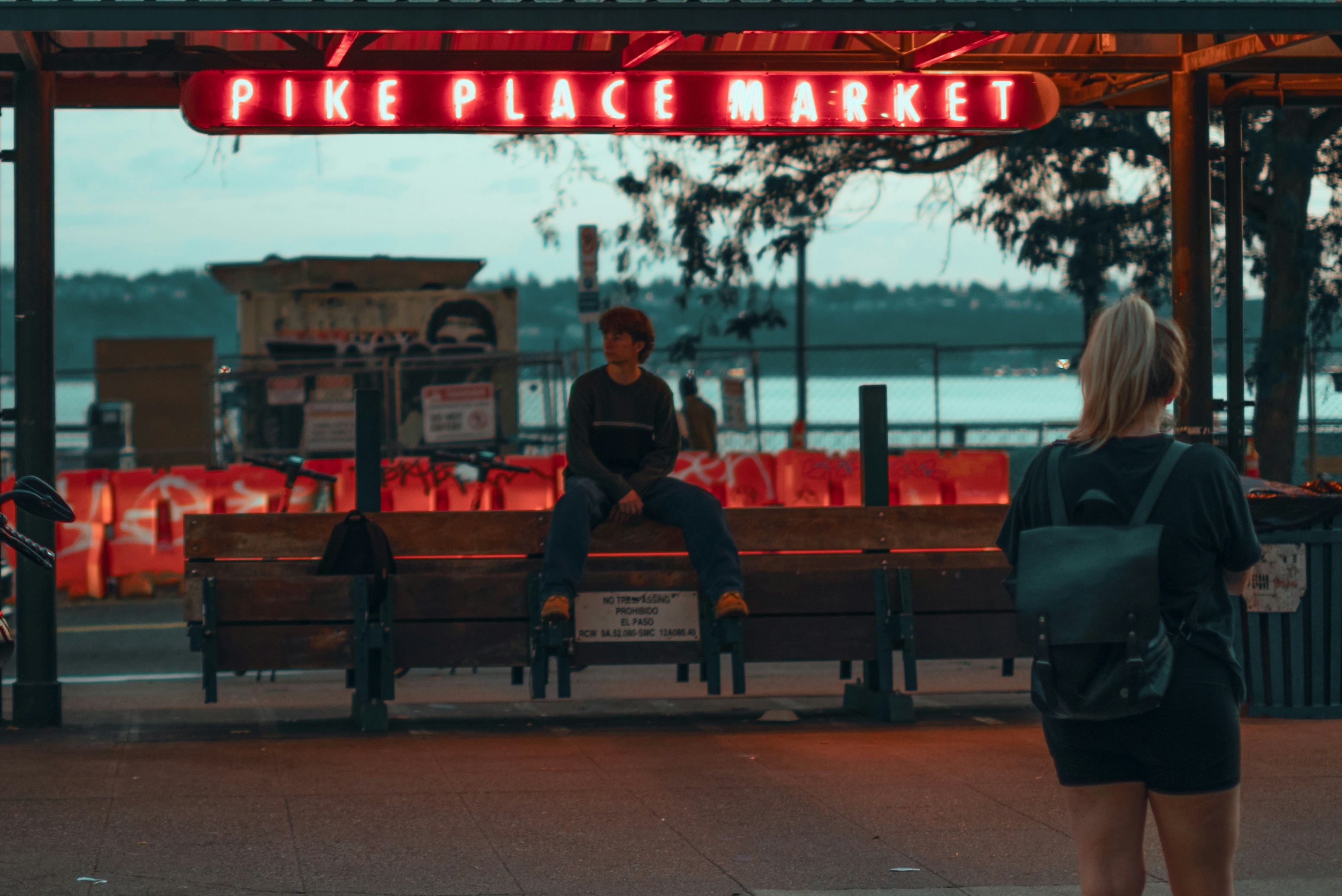 A couple of people sitting on a bench under a neon sign photo – Free ...