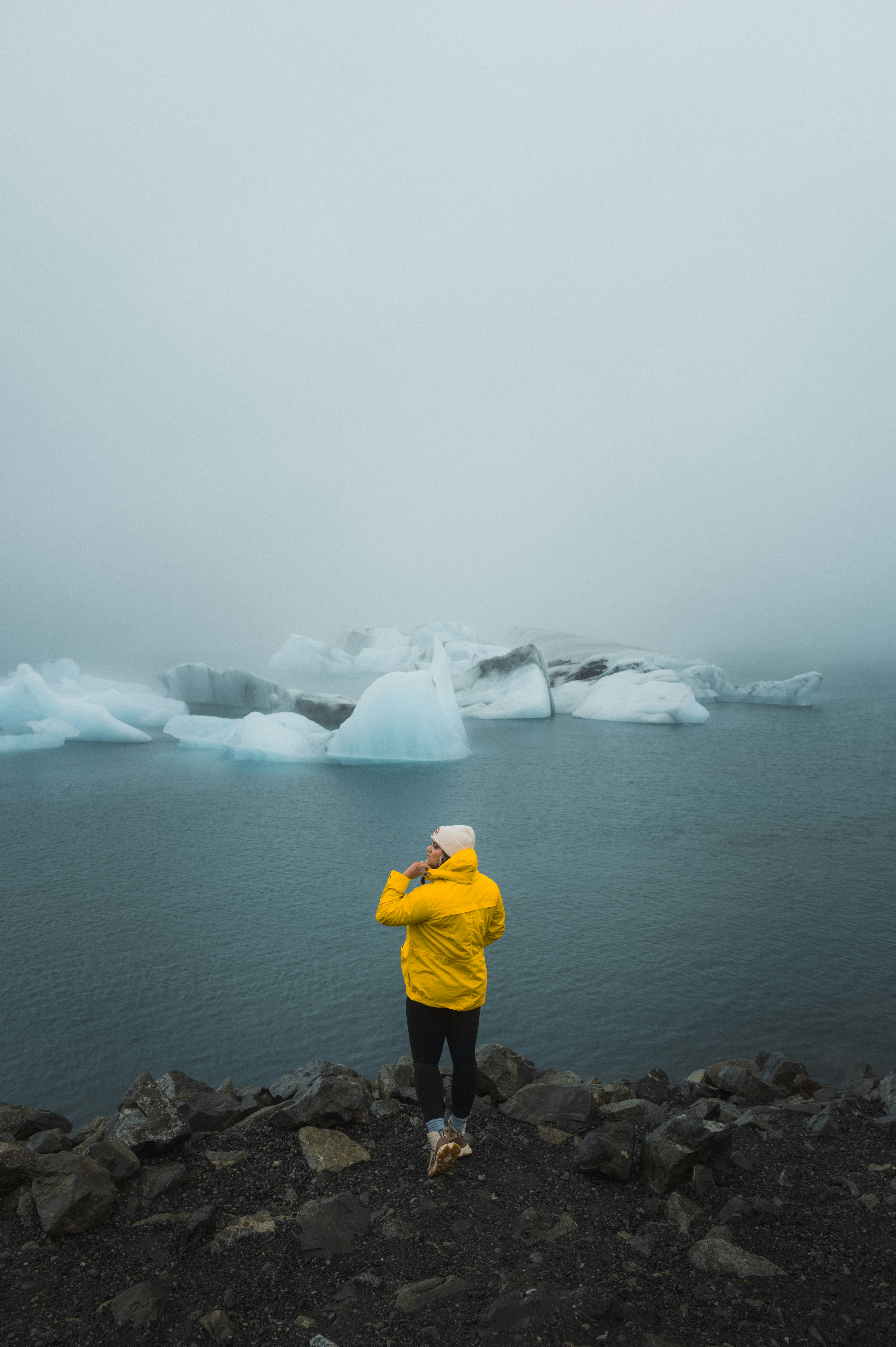 A person in a yellow jacket standing on a rocky shore photo – Free ...