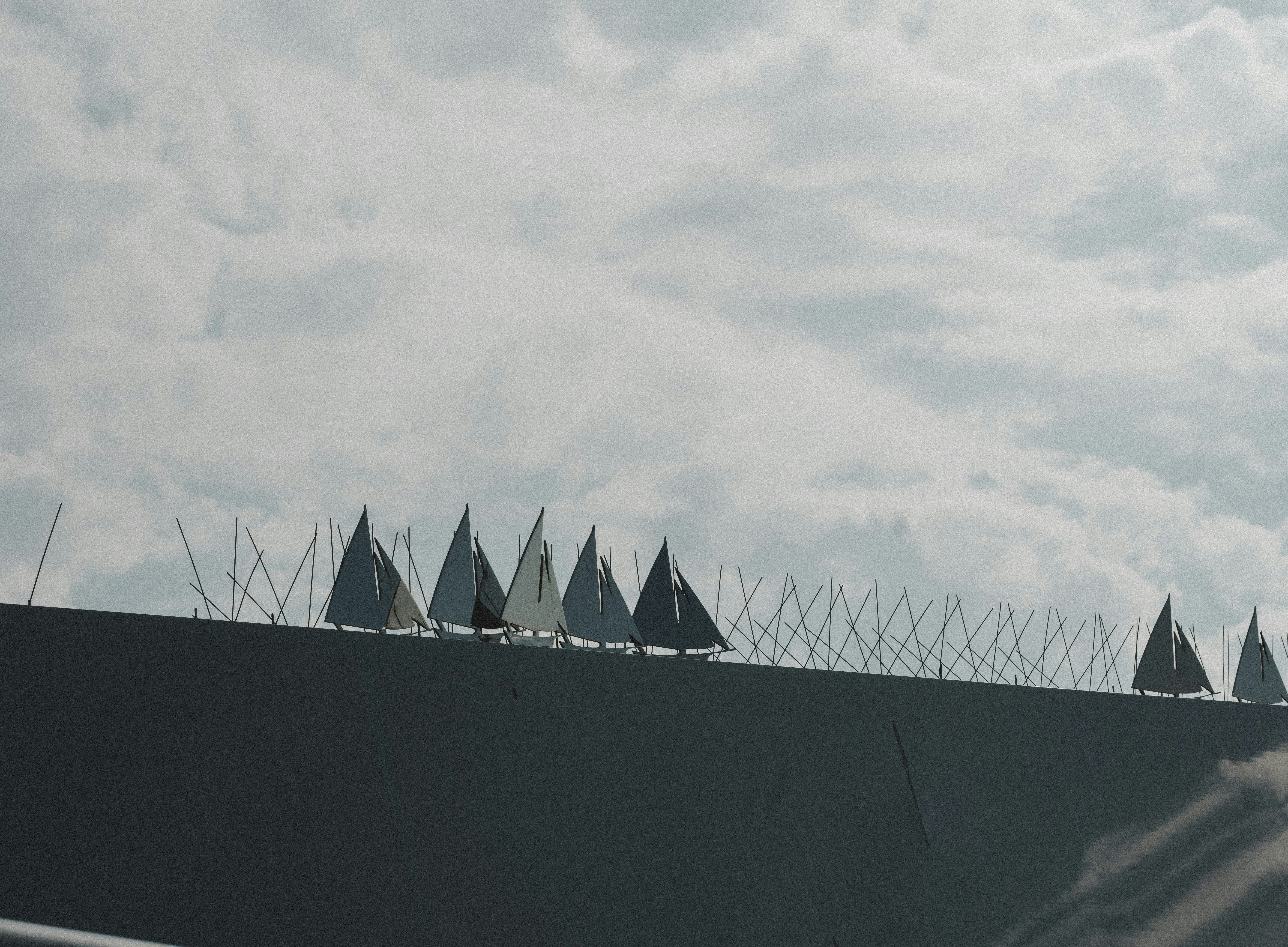 Roofline Sails: Triangular silhouettes lining a rooftop under cloudy skies