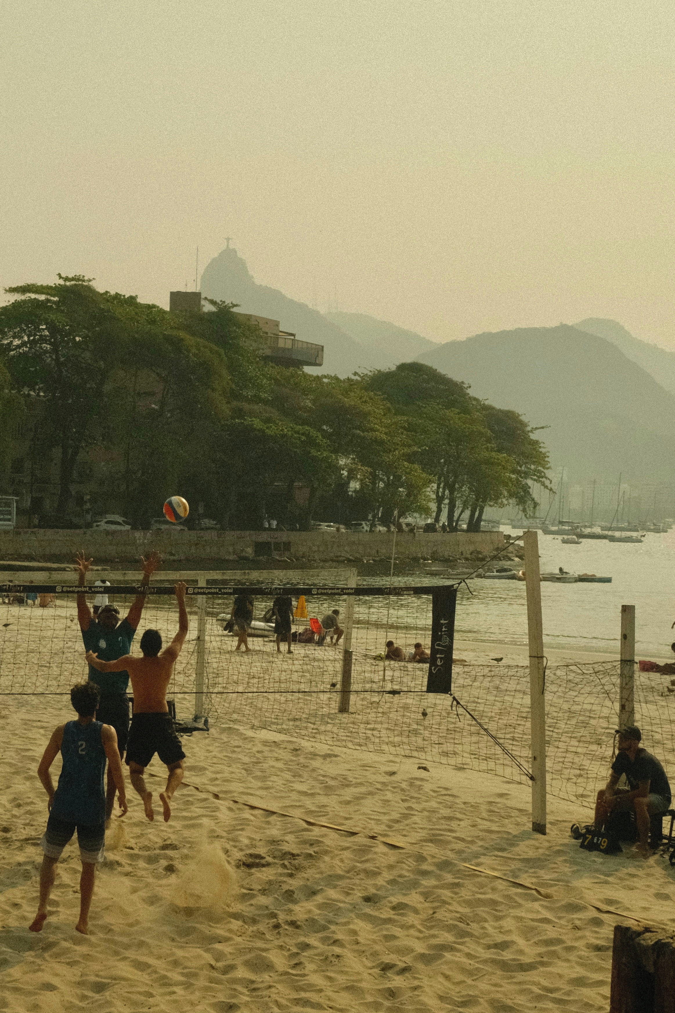 Sunlit Jumpers: Beach Volleyball by a Harbor in hazy golden light