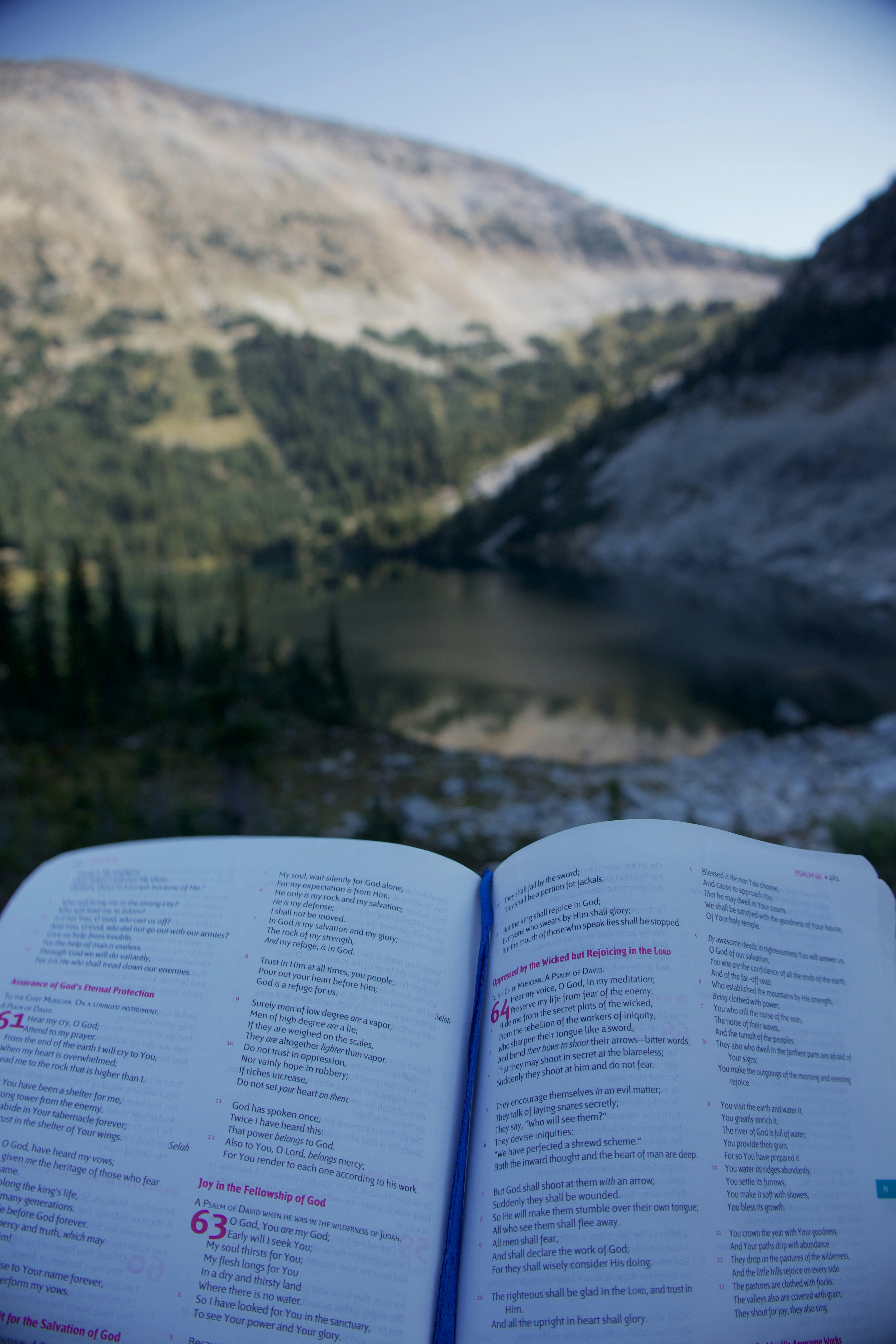 Open book resting on a rocky surface with natural scenery in the background, blending spirituality and wilderness. The serene landscape complements the text within.