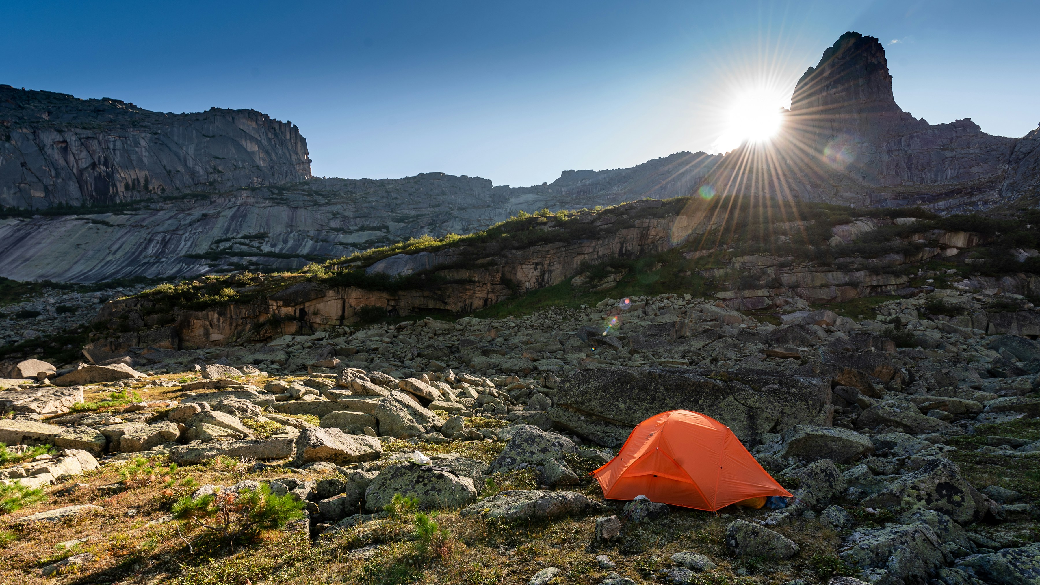 Sunburst over a rugged amphitheater: a lone orange tent anchors the rocky expanse
