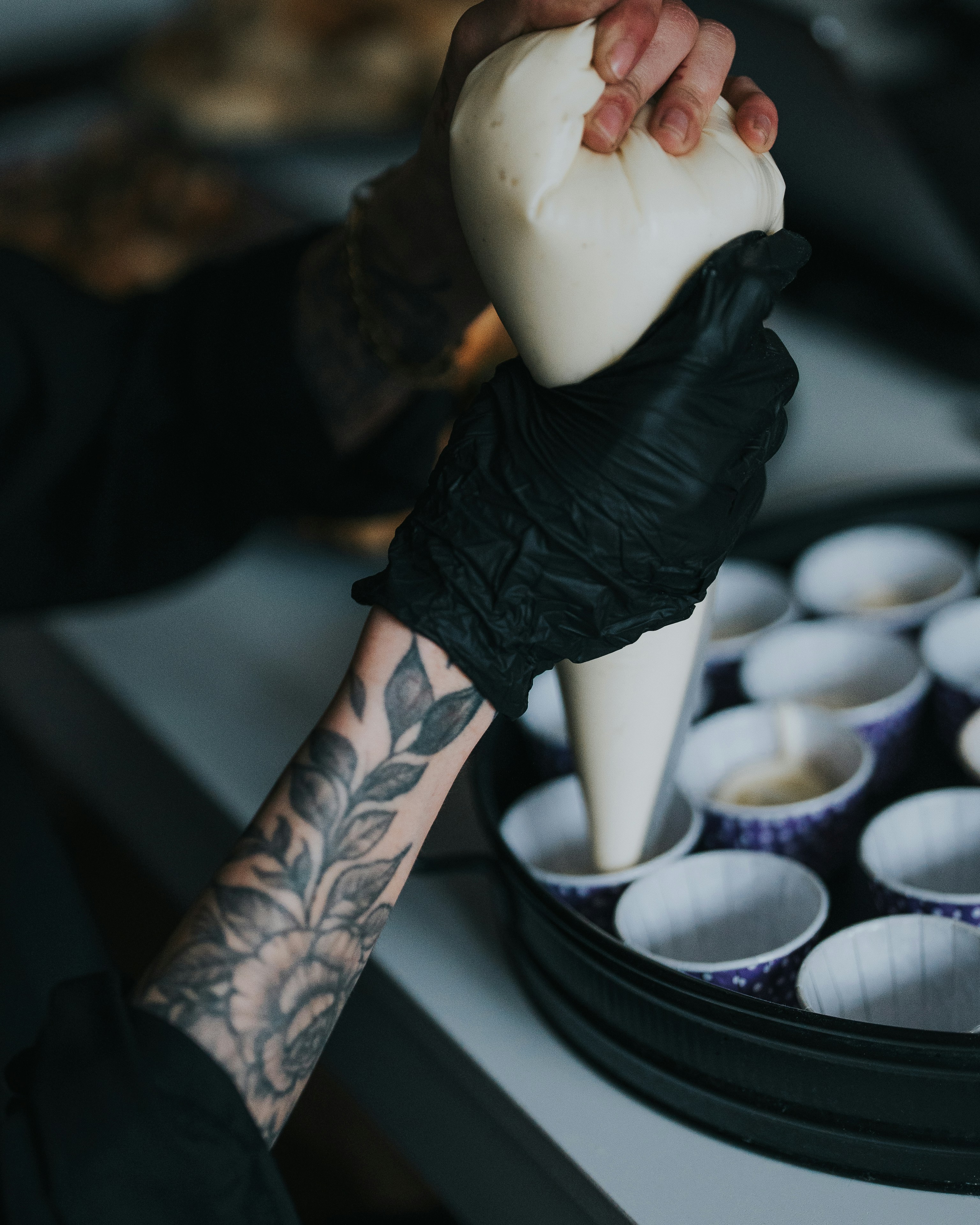 Tattooed Arm Piping Batter into Purple-Rim Muffin Cups